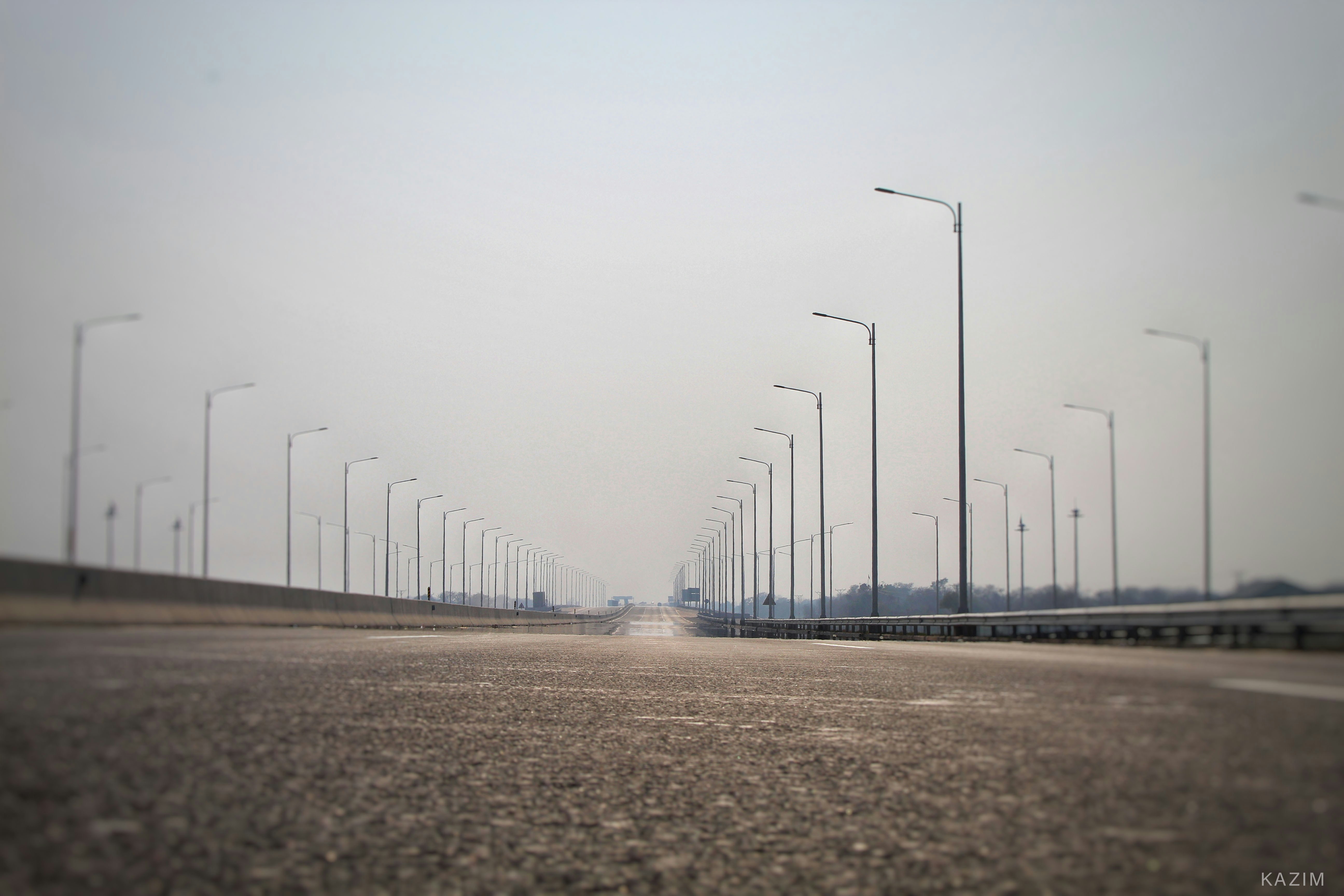 Long stretch of empty motorway flanked by rows of streetlights under a pale sky.