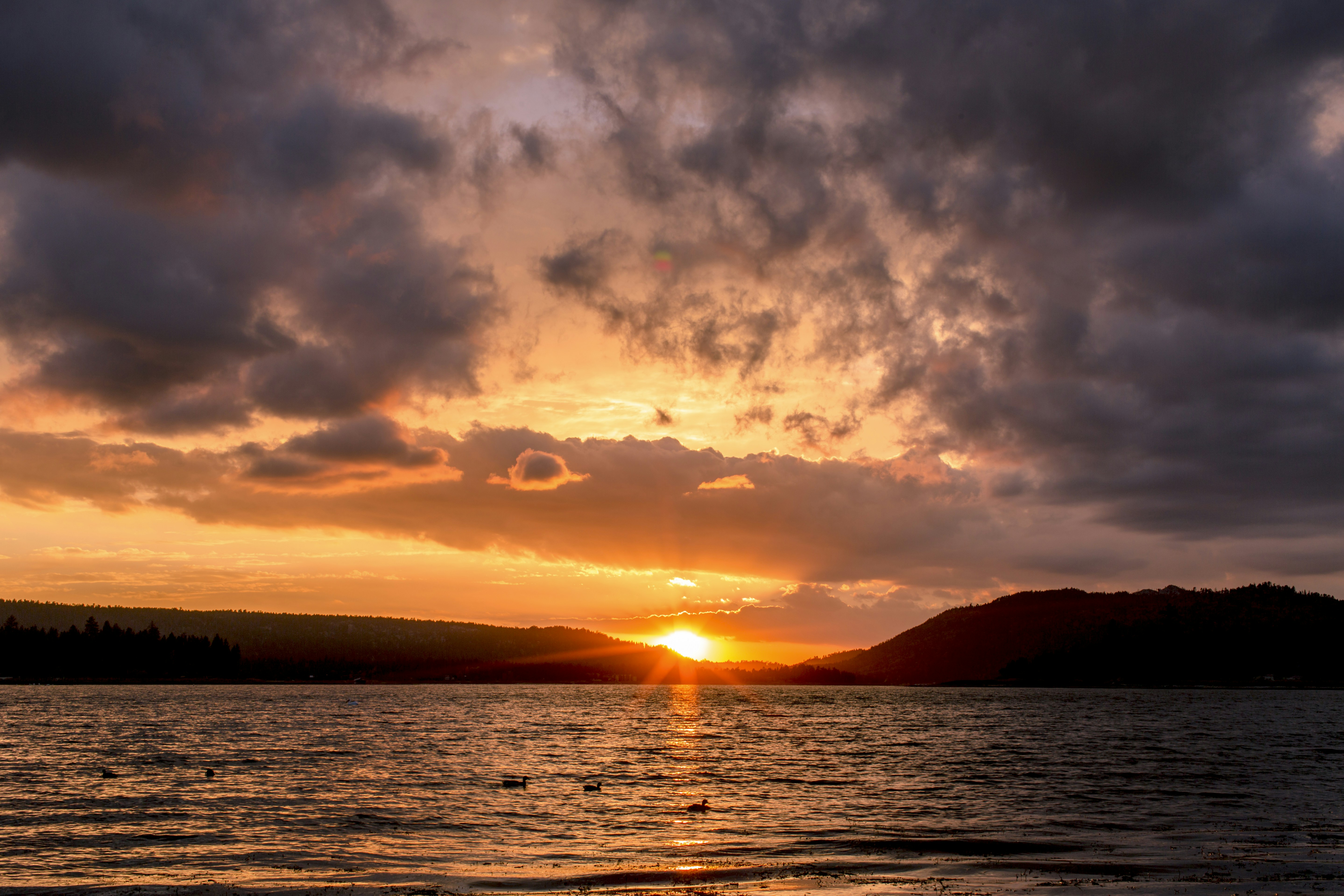 Golden sunset illuminating a serene lake surrounded by hills and dramatic clouds.