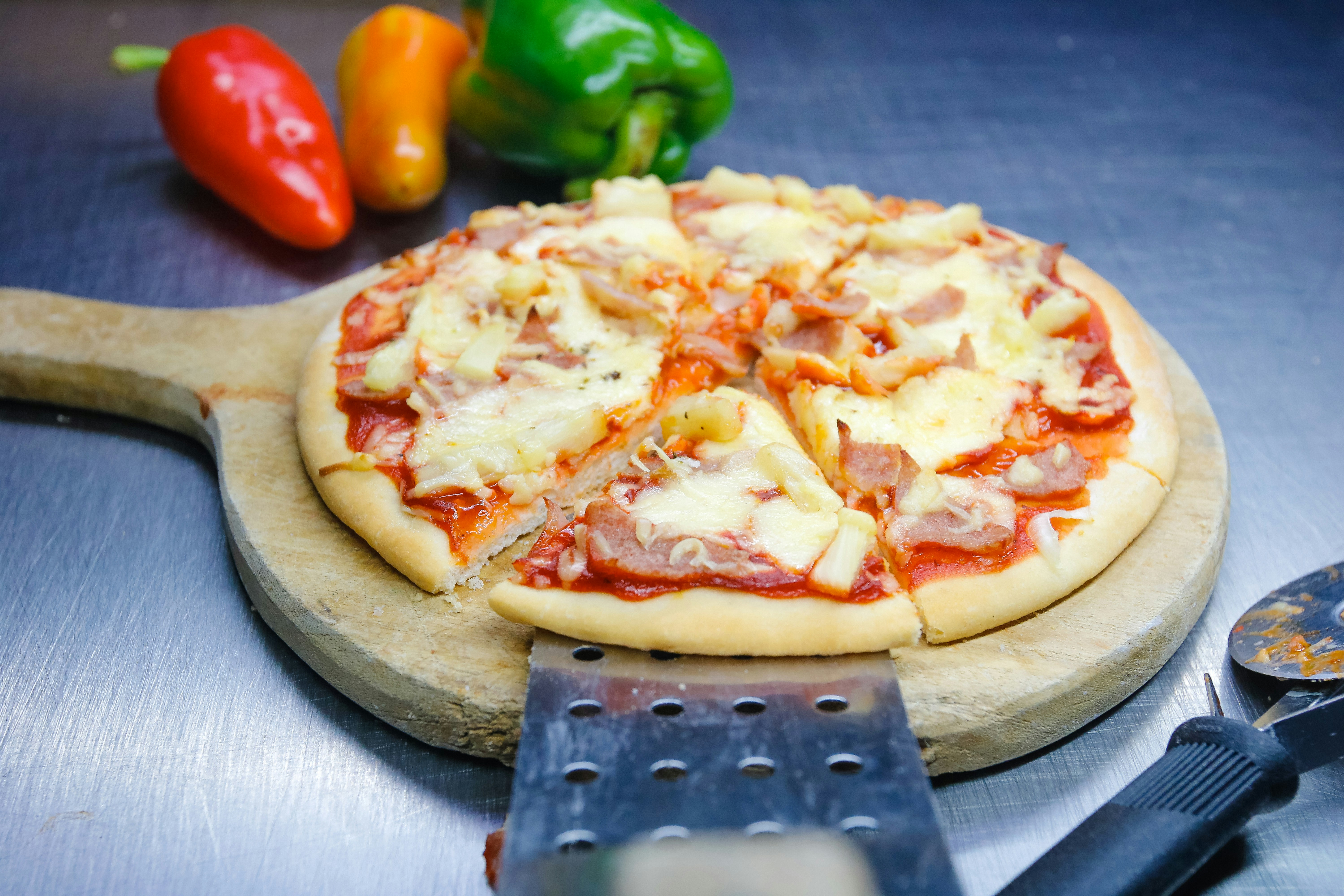 Freshly baked pizza on a wooden paddle surrounded by colorful bell peppers.