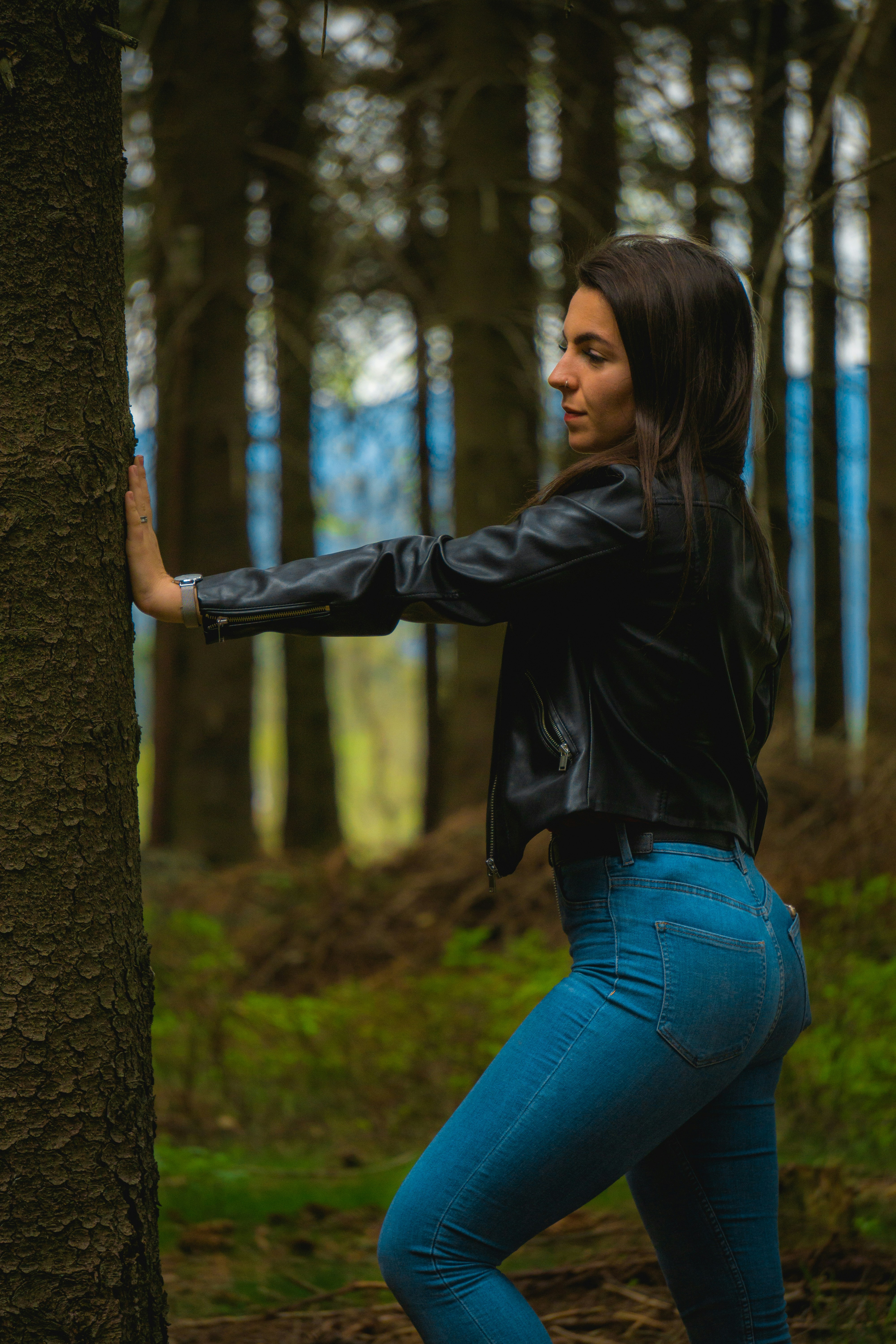 Woman in black long sleeve shirt and blue denim jeans leaning on tree ...