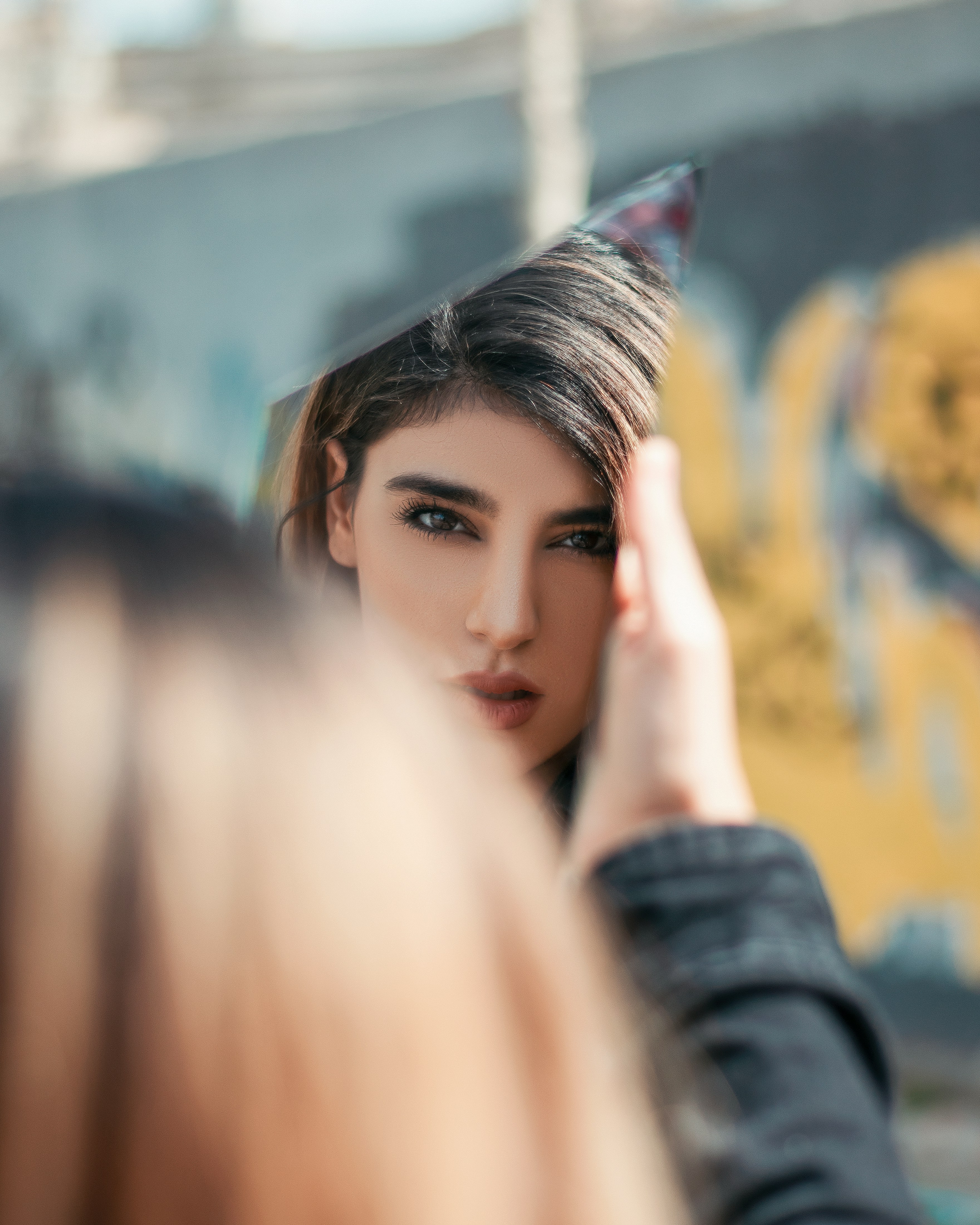 A young woman gazes intently at her reflection in a mirror, framed by vibrant graffiti. The scene captures a blend of urban art and personal contemplation.