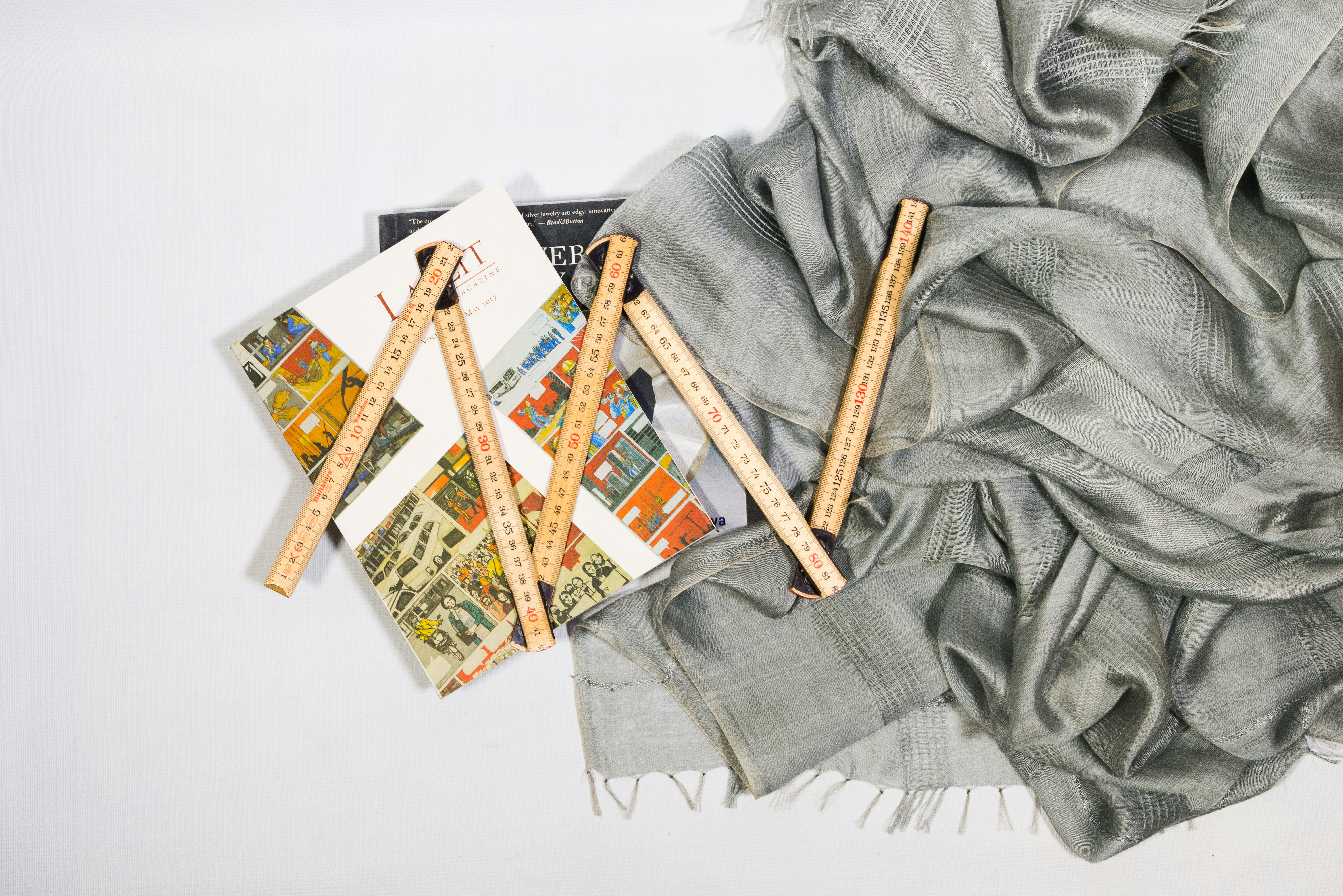Flat lay photograph showcasing vintage comic cards fanned with wooden rulers over a soft gray scarf.