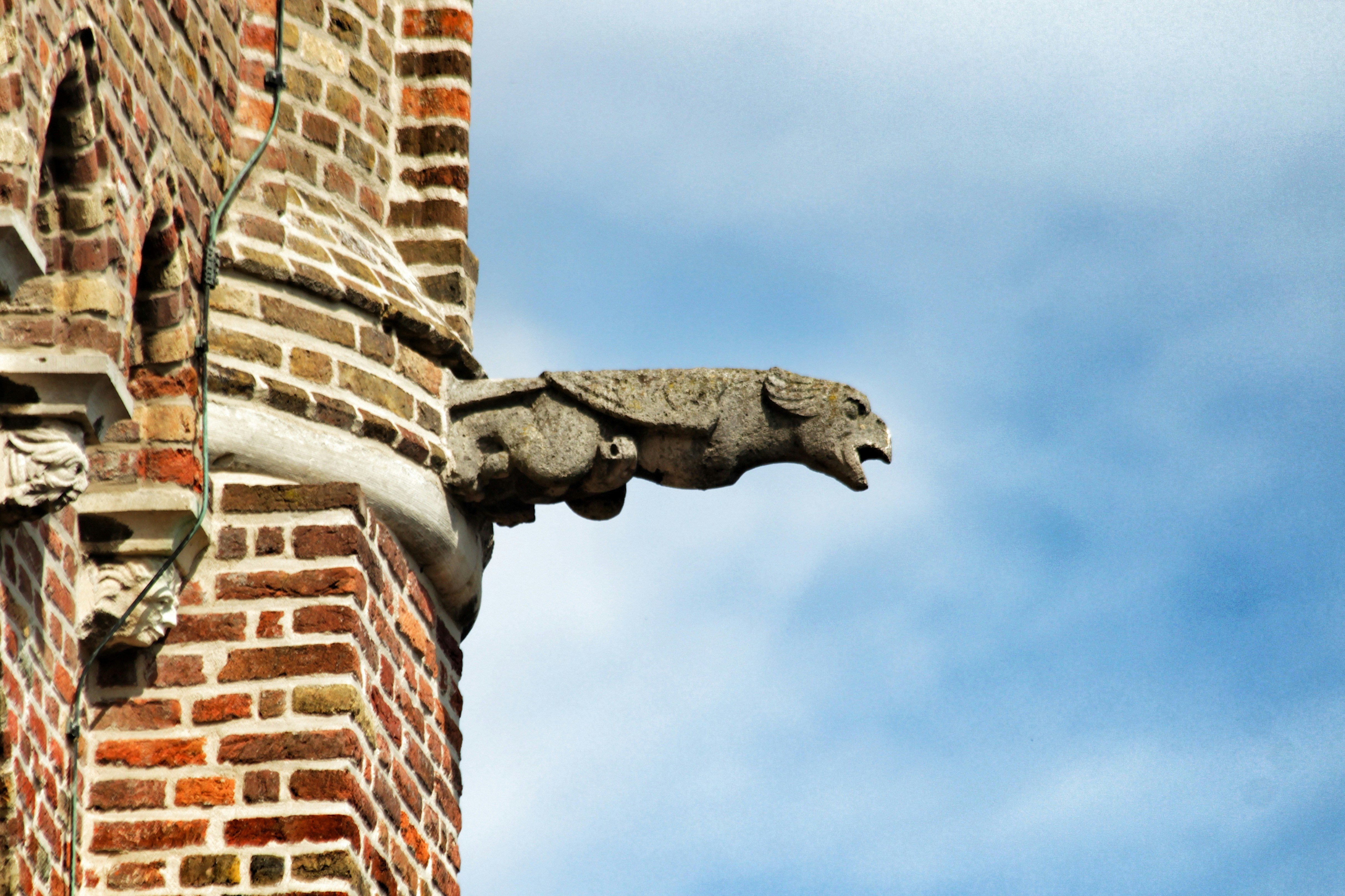 Stone gargoyle juts from intricate brickwork against a vivid blue sky.