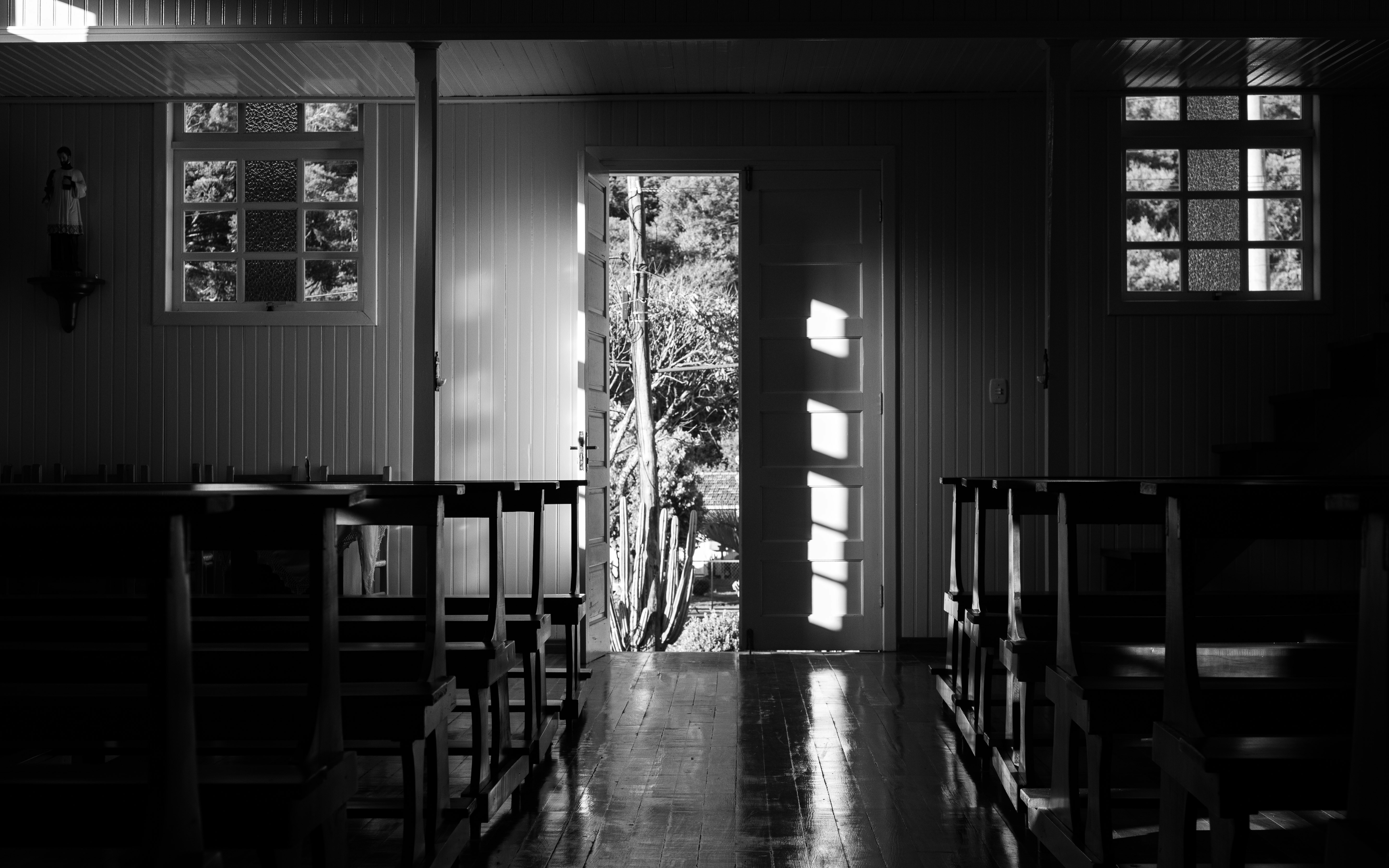 Sunlight streams through an open doorway, casting patterned shadows on the floor inside a dimly lit room.