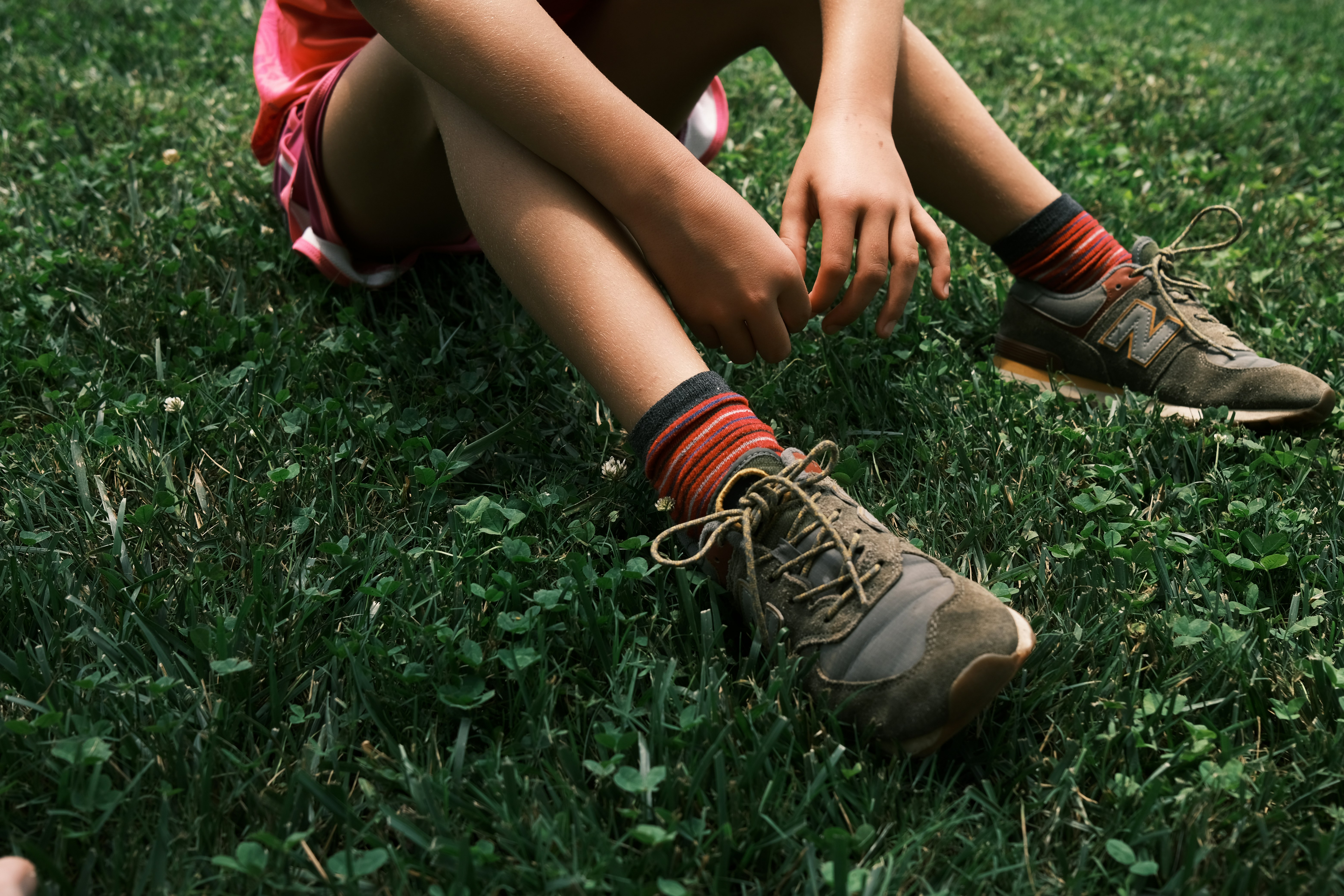 A close-up view of a person's legs resting on grass, showcasing stylish sneakers and vibrant socks. The relaxed pose invites a sense of tranquility.