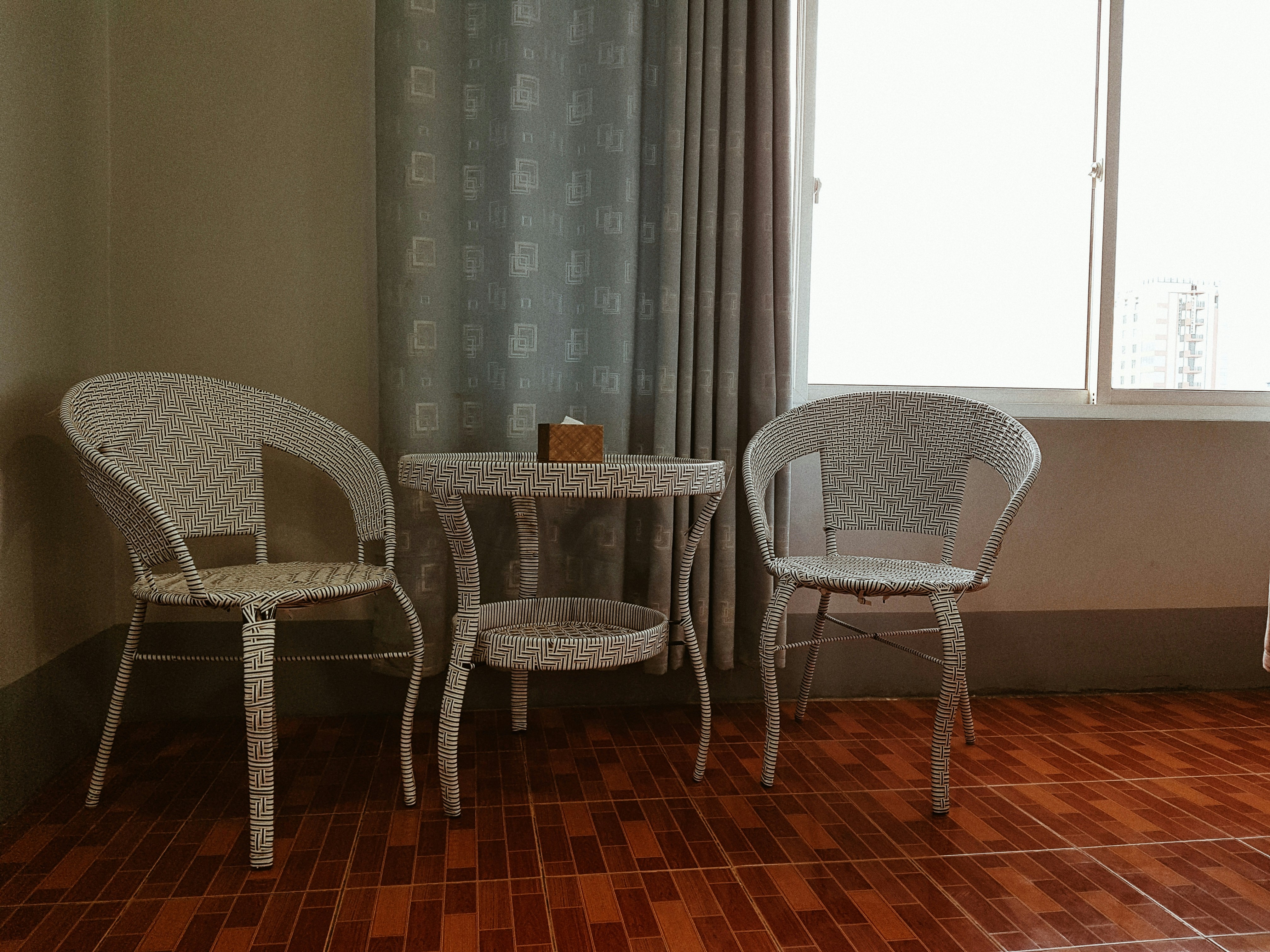 Two white wicker chairs and a small table create a tranquil seating area in a softly lit room with patterned curtains.