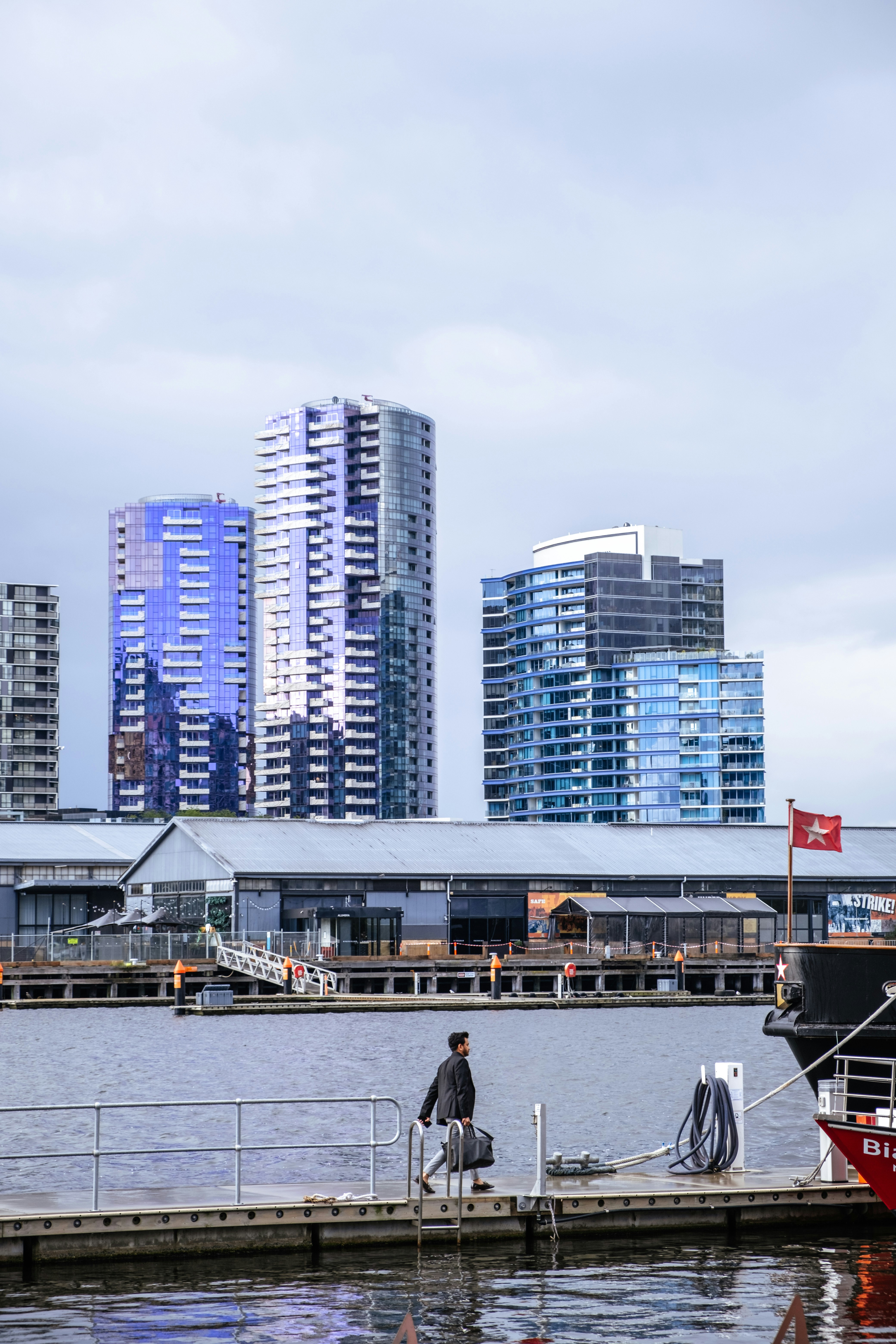 Lone Walker on the Pier as Blue Glass Towers Rise