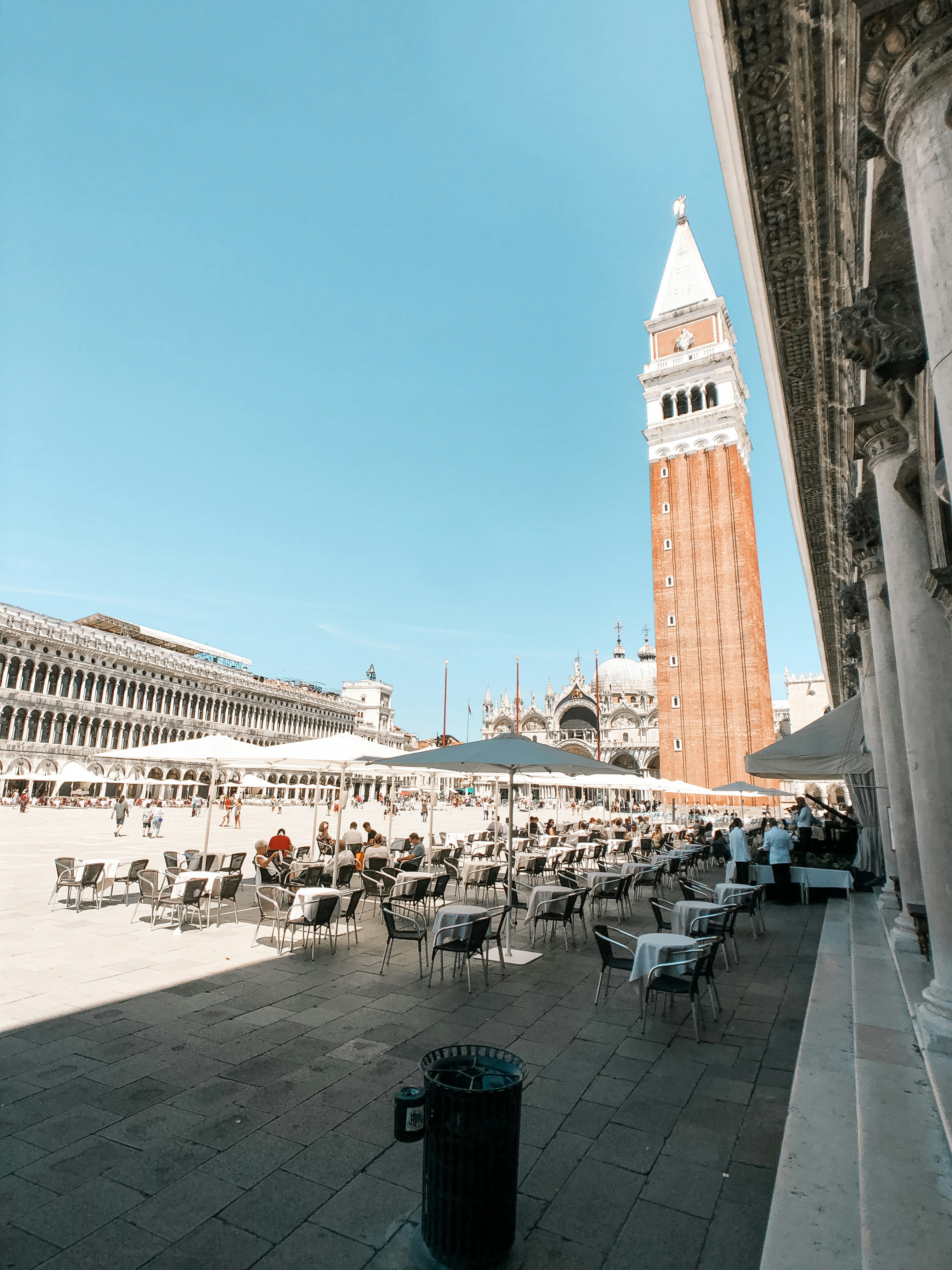 Vibrant scene in St. Mark's Square, showcasing outdoor seating and the iconic Campanile tower against a clear blue sky.
