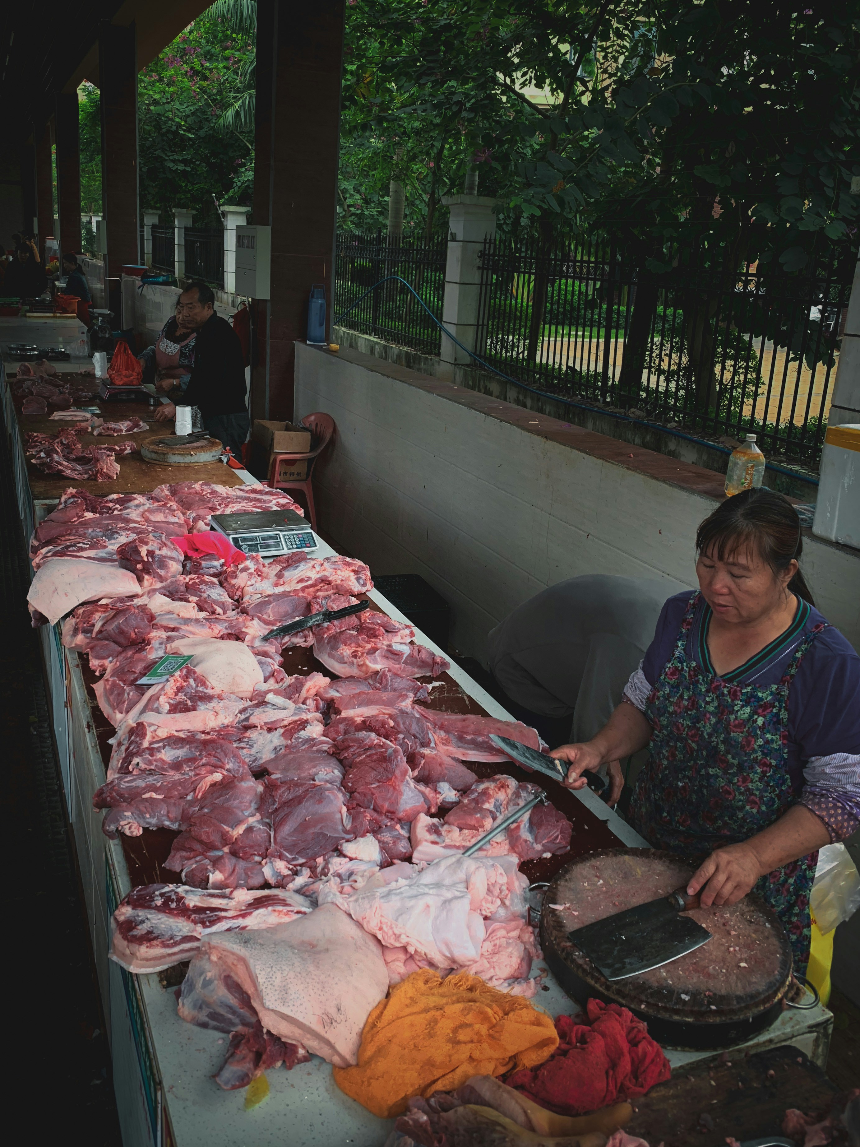 Butcher at a busy market stall skillfully arranging various cuts of meat, surrounded by a vibrant atmosphere of local commerce.