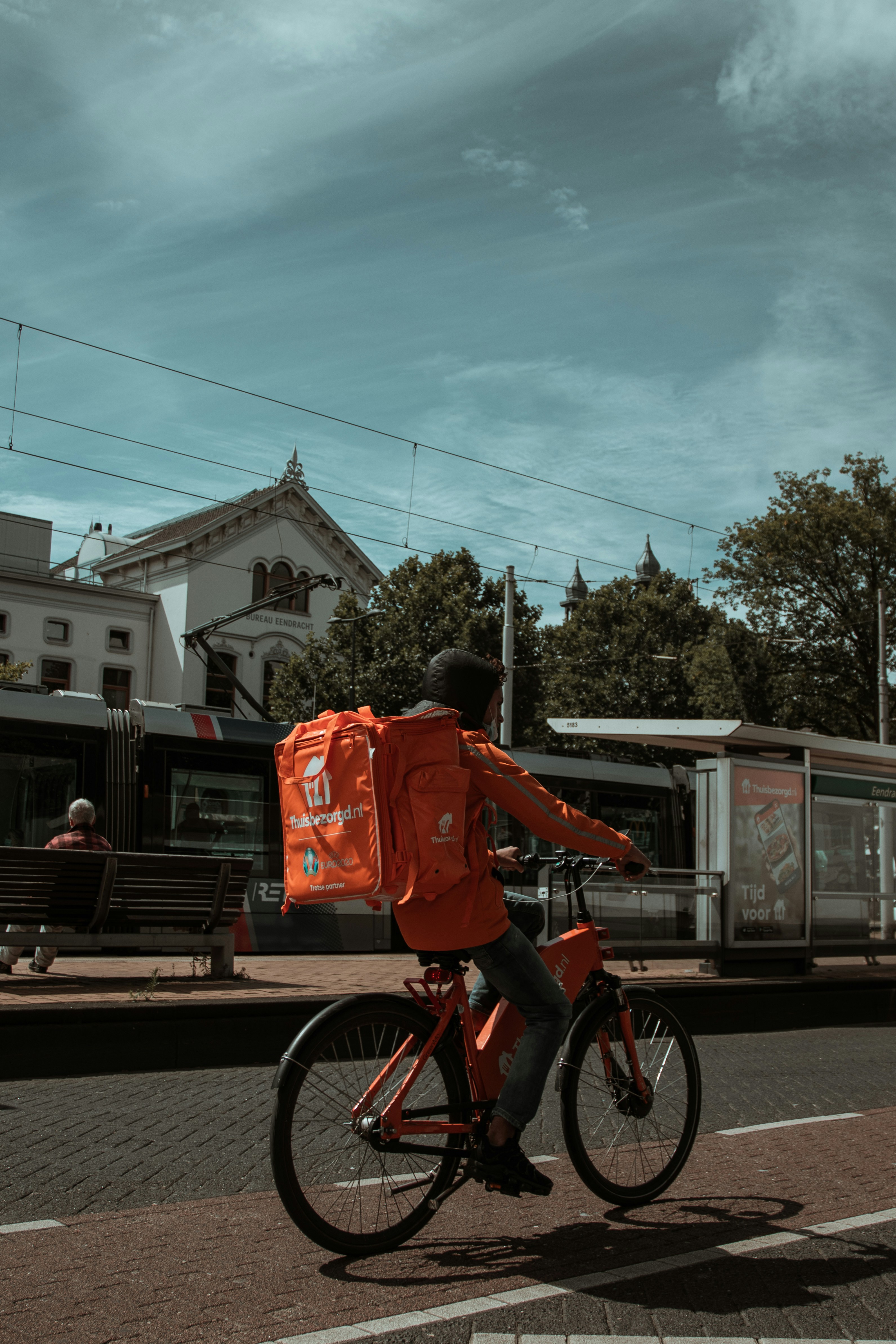 Orange-Clad Cyclist at a Sunlit City Tram Stop