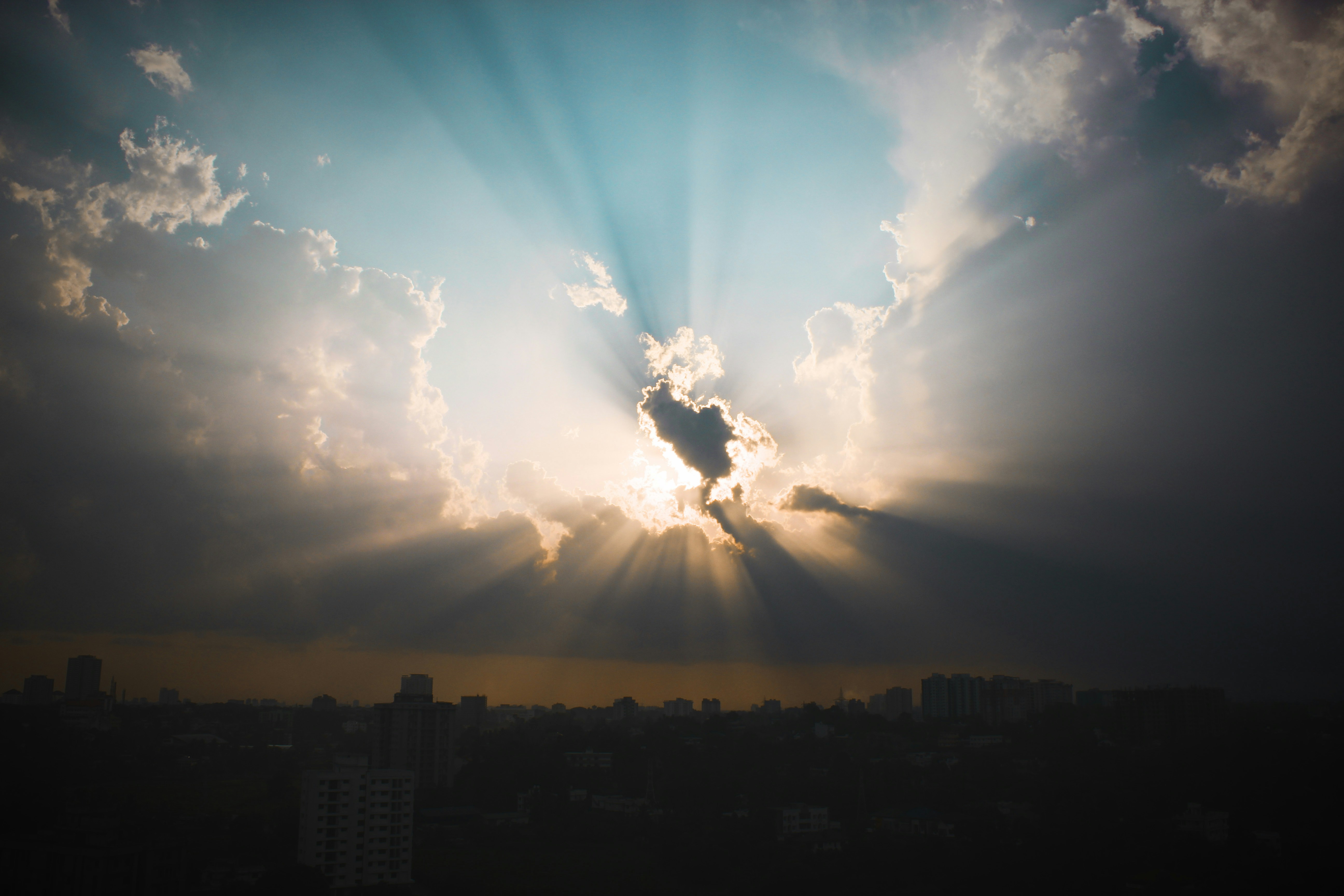 Sunlight breaks through dramatic clouds, casting rays over a city skyline at dusk.