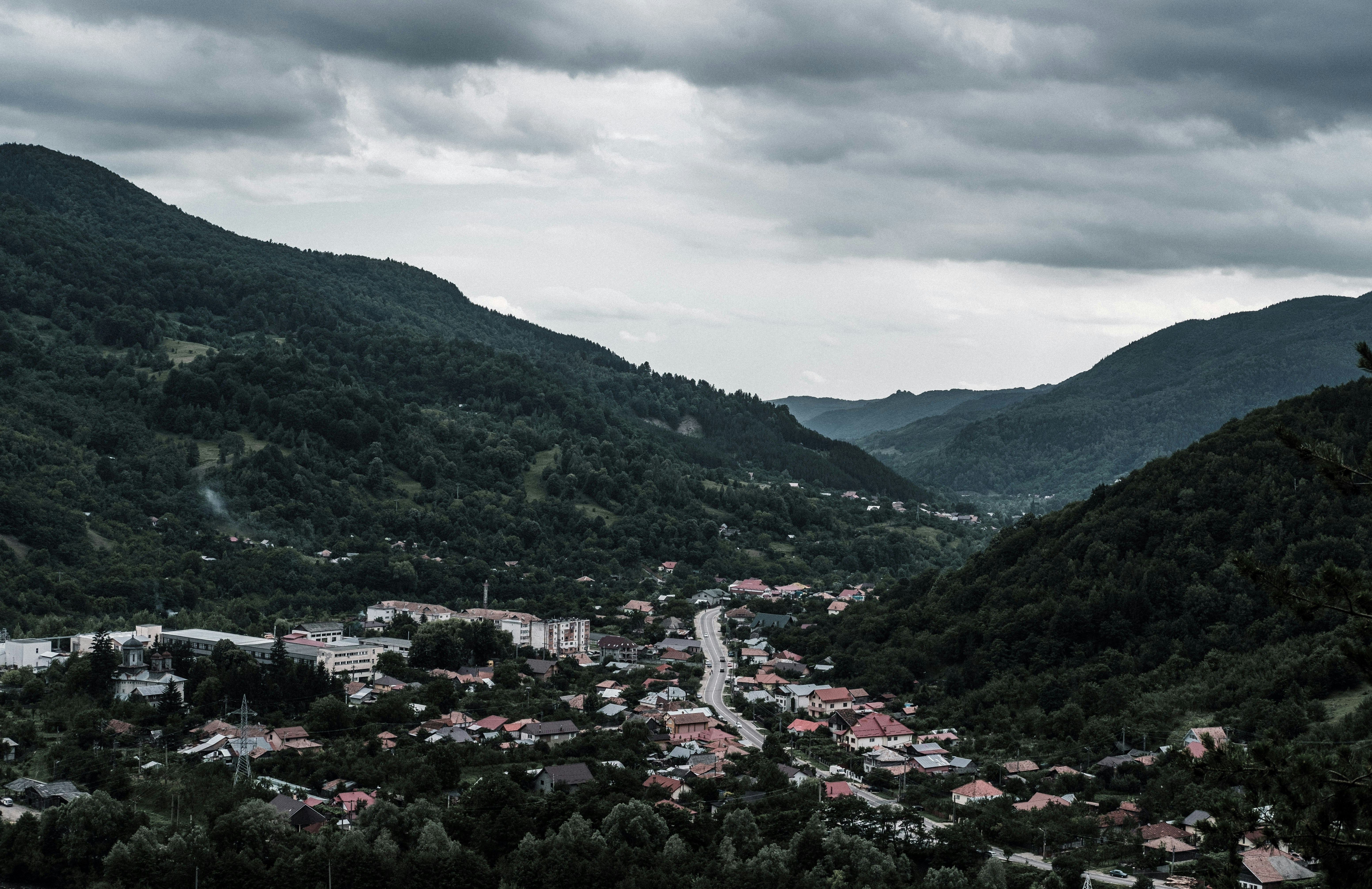 A serene valley town nestled between rolling hills, with winding roads and scattered homes under a moody sky.