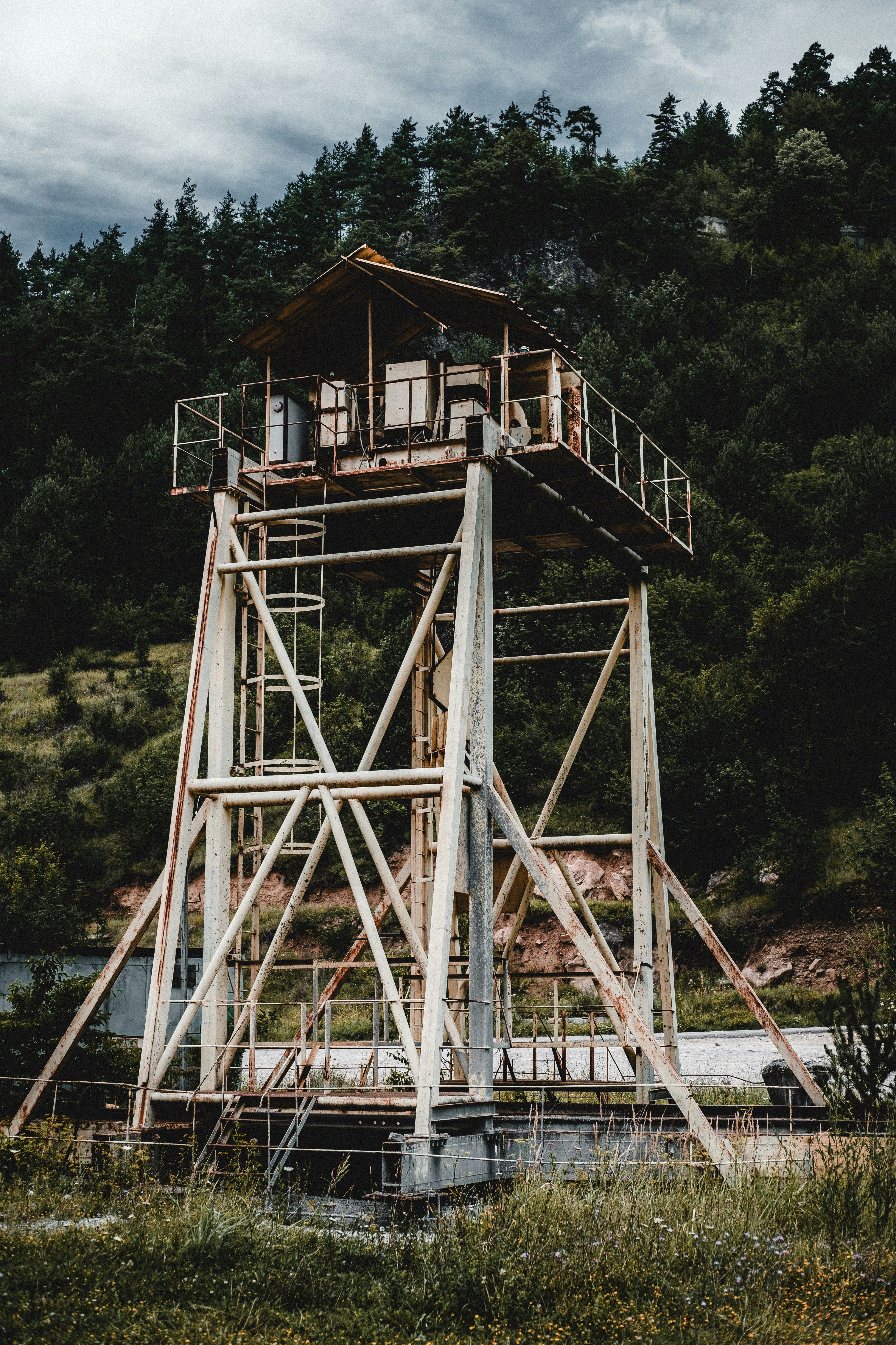 Abandoned watchtower stands resilient amidst overgrown greenery, showcasing the passage of time in a once-bustling industrial site.