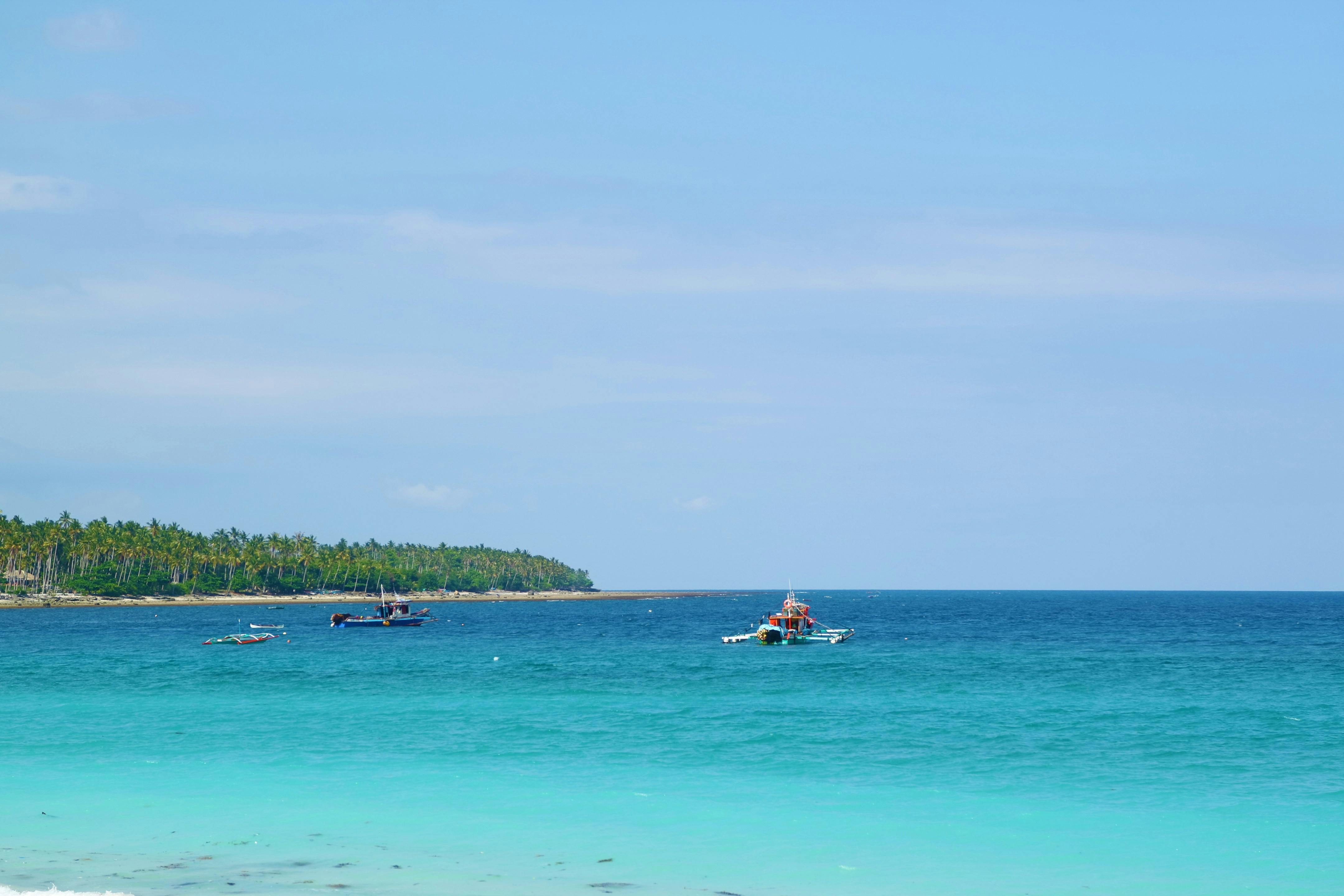 Small boats floating on a serene turquoise sea under a clear blue sky.