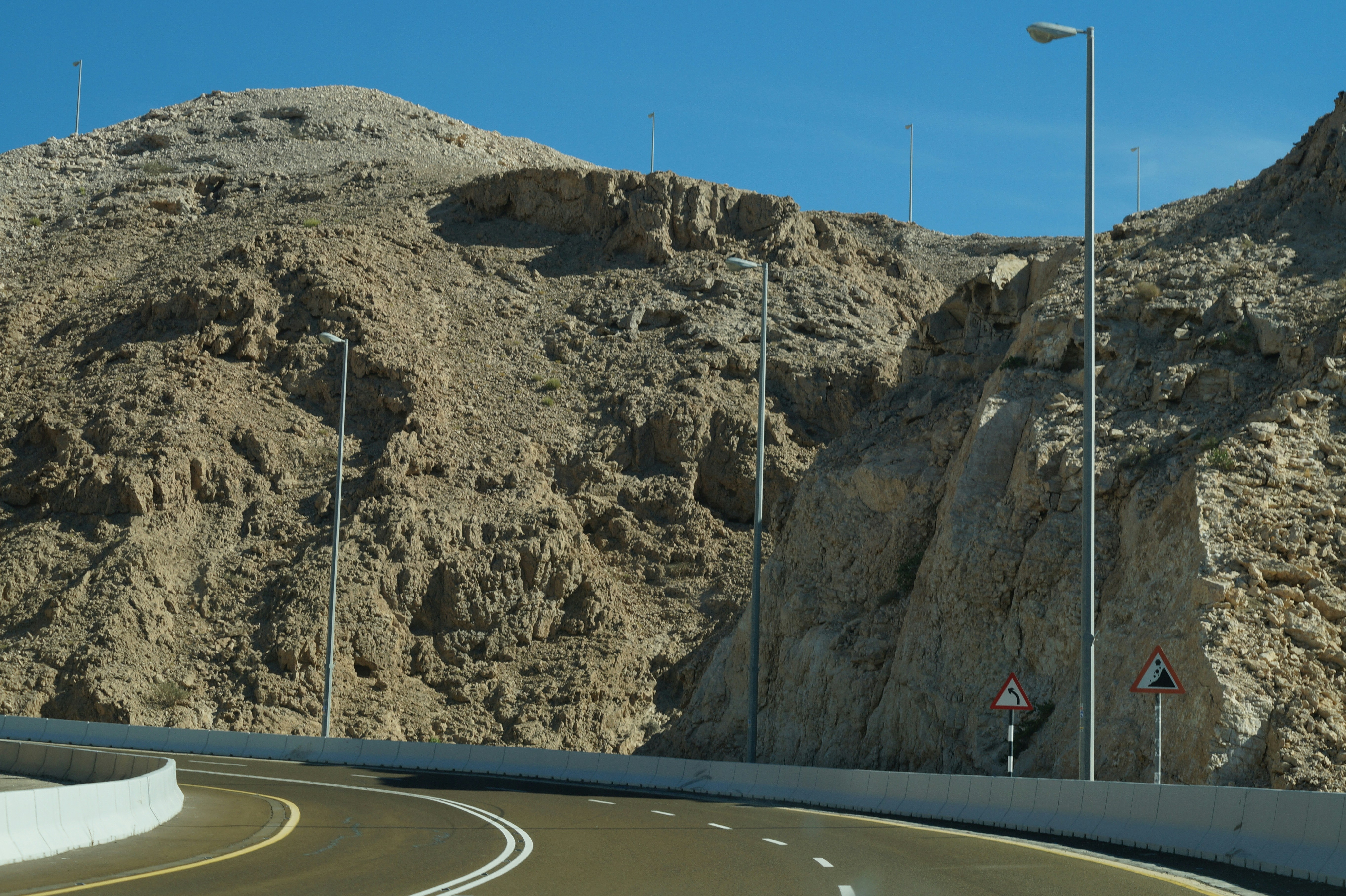 Curved roadway navigating through rugged, rocky landscape under a clear blue sky.