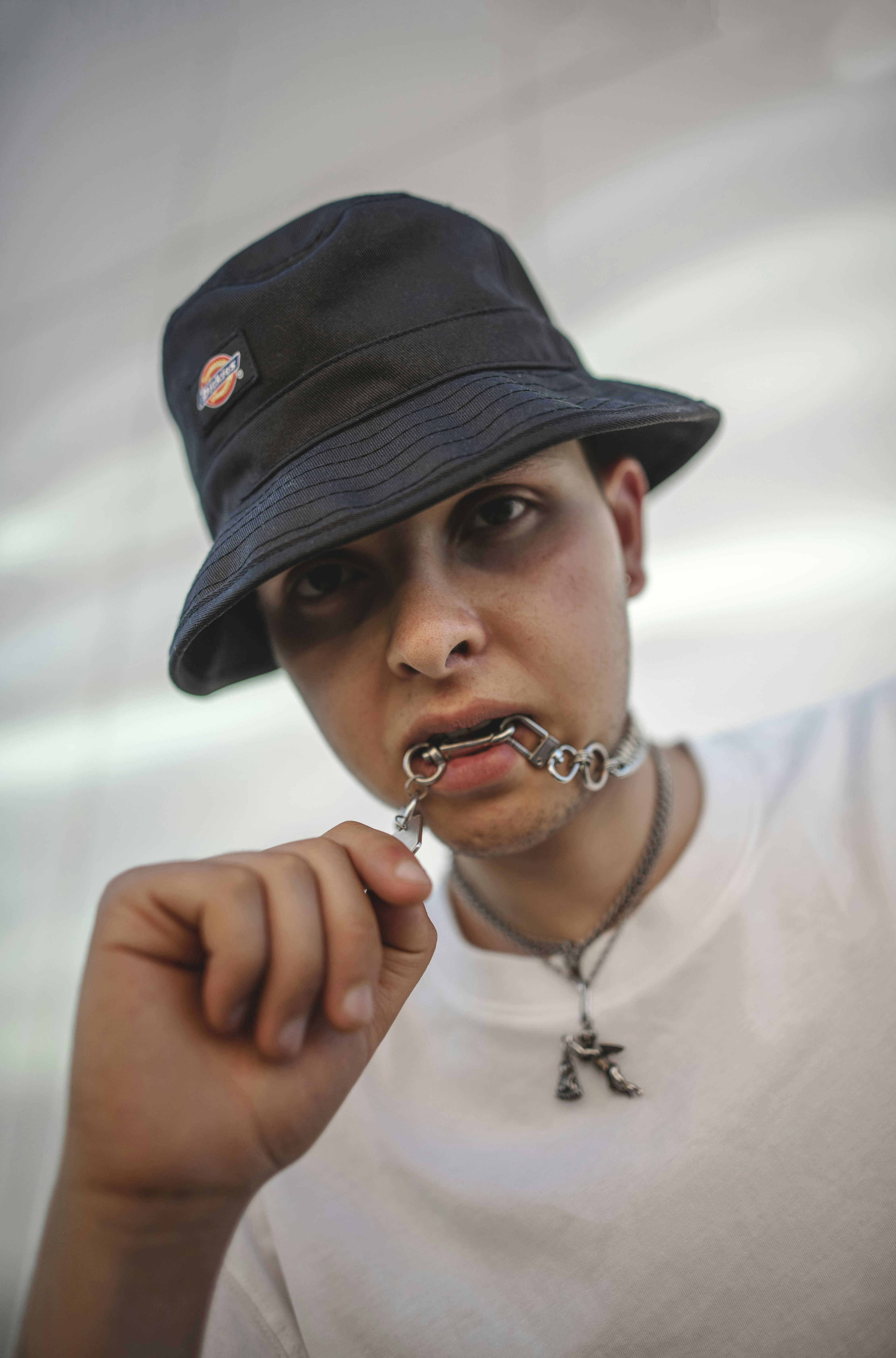 Chin-strap poise: a close-up of a bucket-hatted subject biting a metallic chain