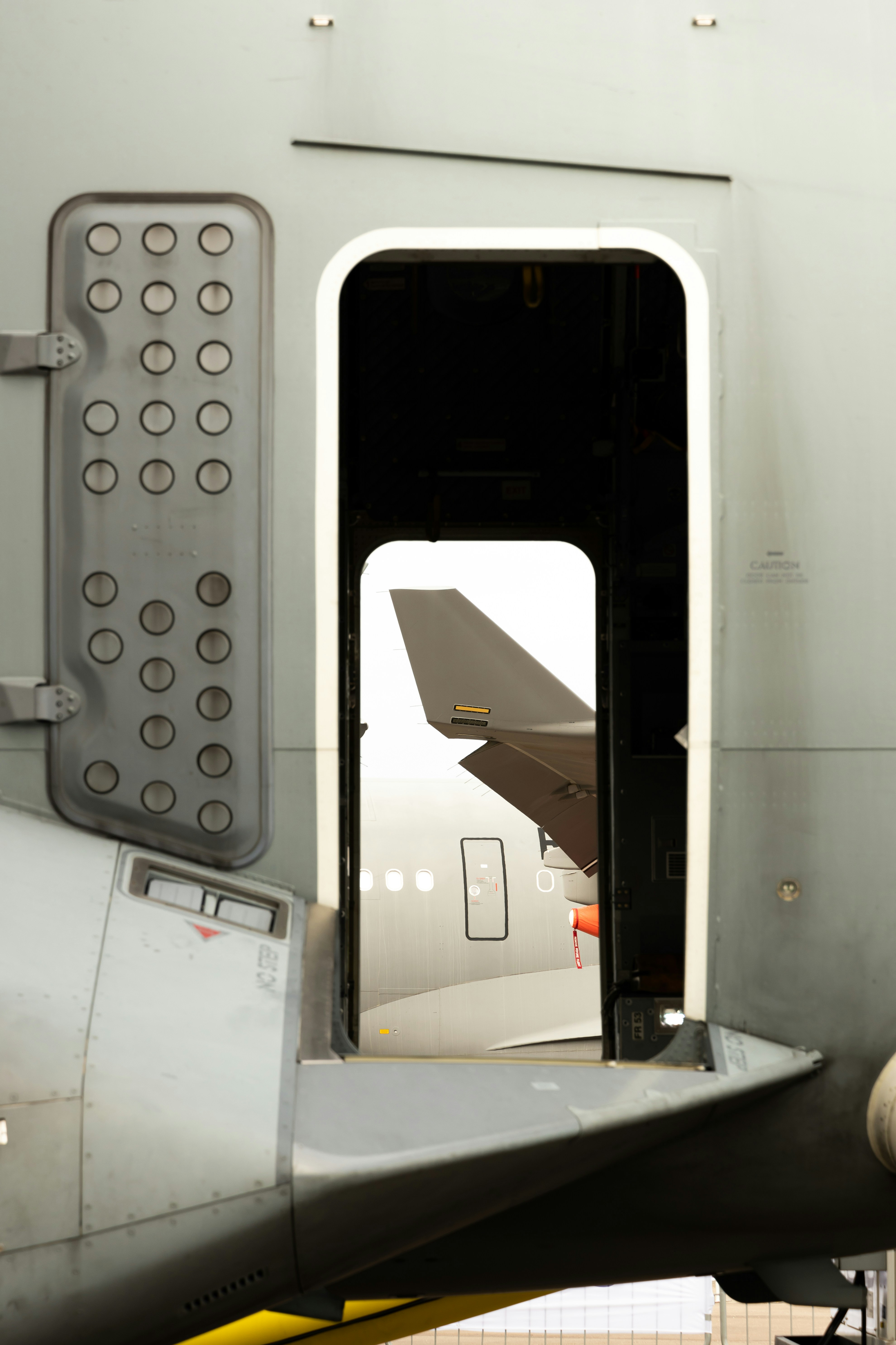 Open cargo door of a military aircraft revealing the tail section of a commercial airliner in the background.