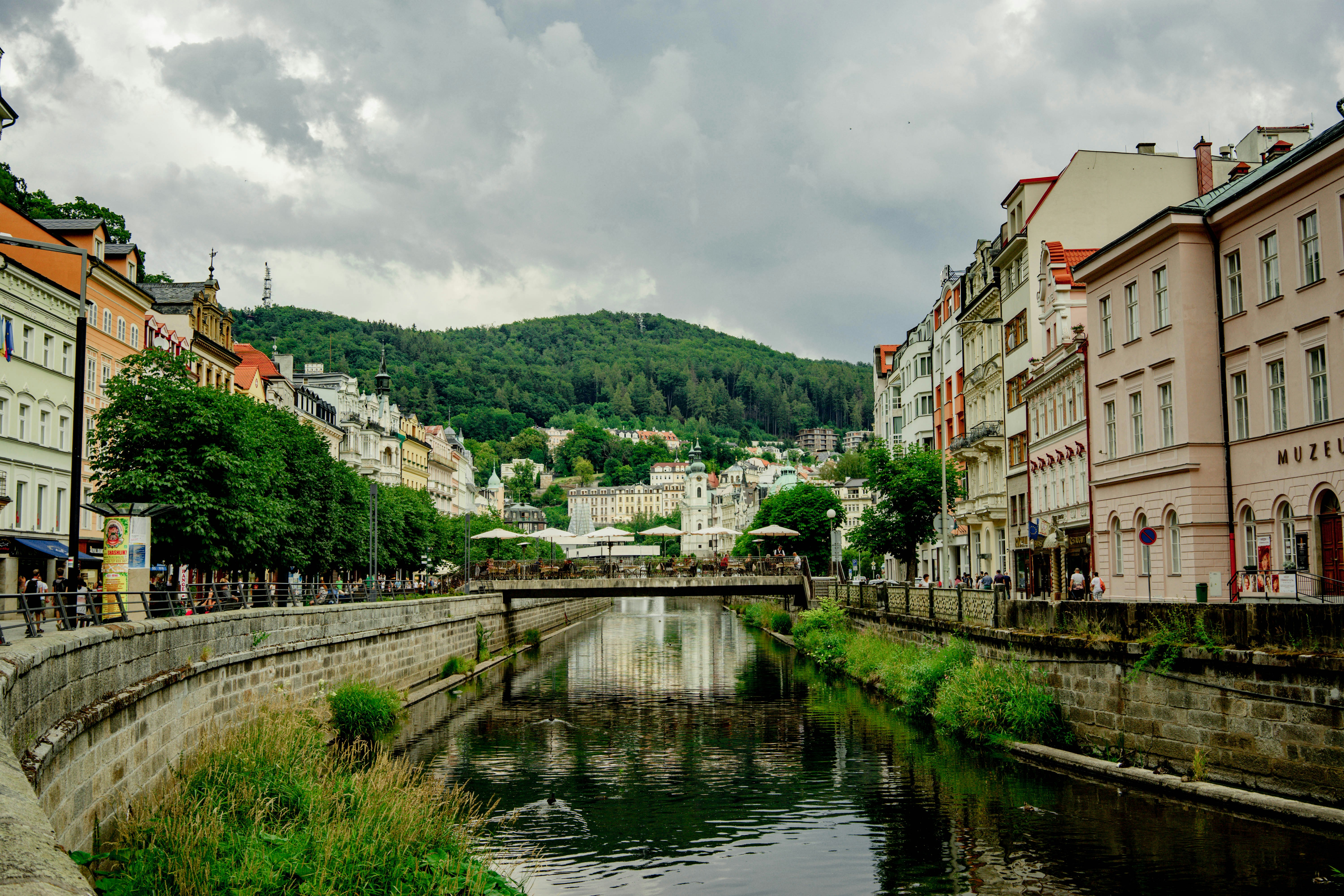 Charming European town with colorful buildings lining a tranquil river under a cloudy sky.
