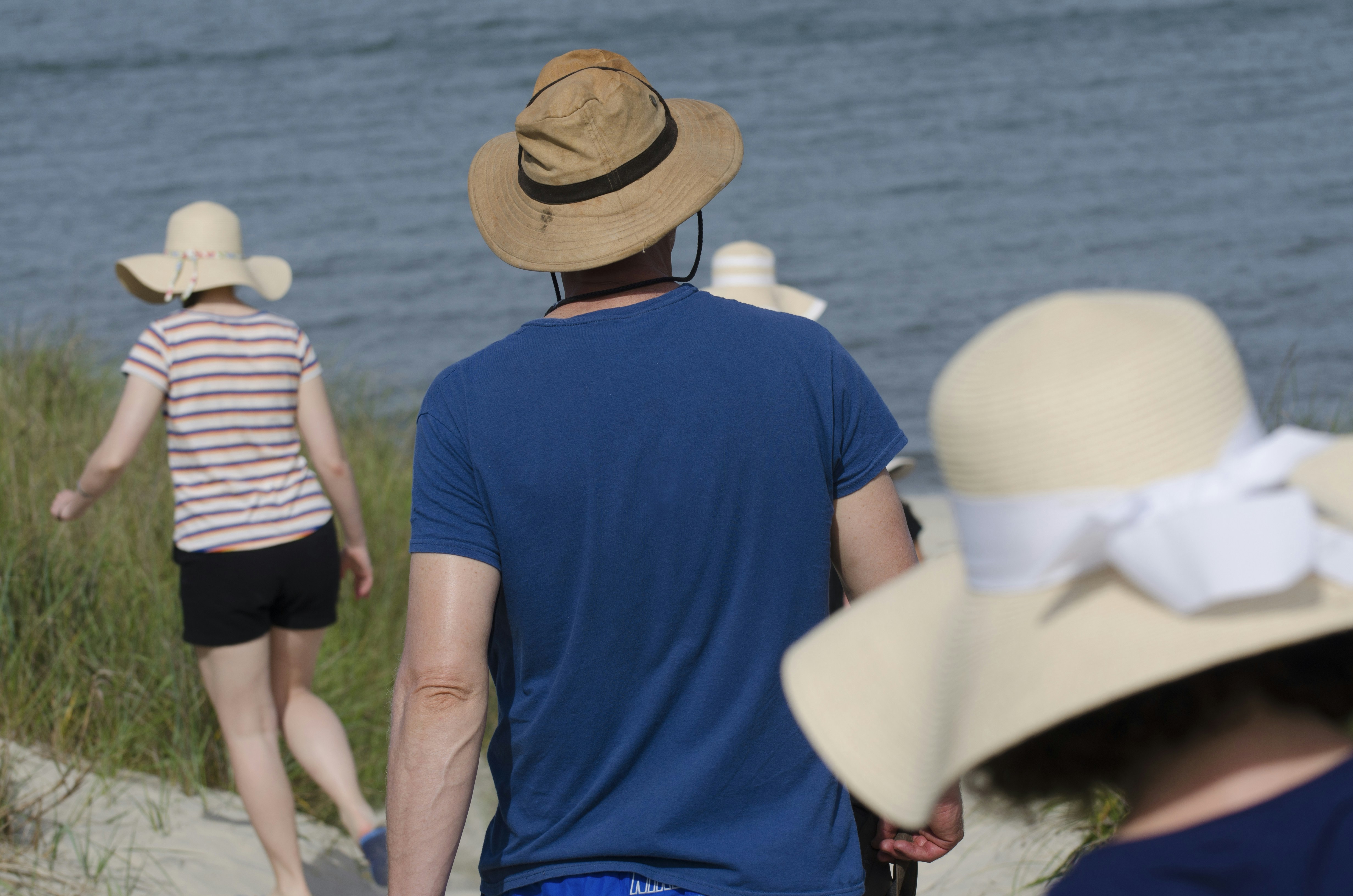 Blue-Shirted Traveler Guides a Hat-Clad Trio Across a Sunlit Beach