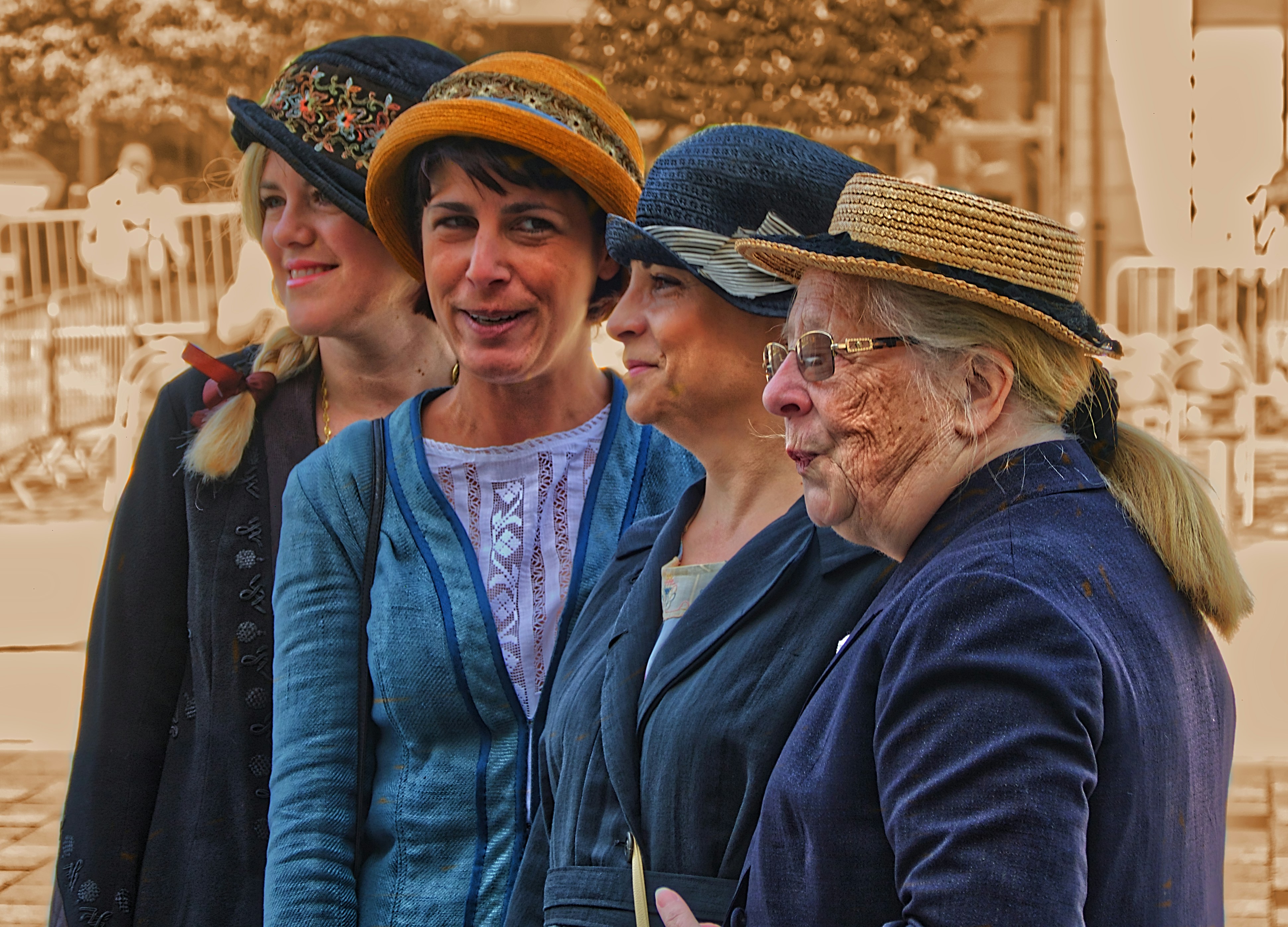 Four women in vintage hats smile together, showcasing a blend of styles and eras. The scene captures a moment of camaraderie and nostalgia.