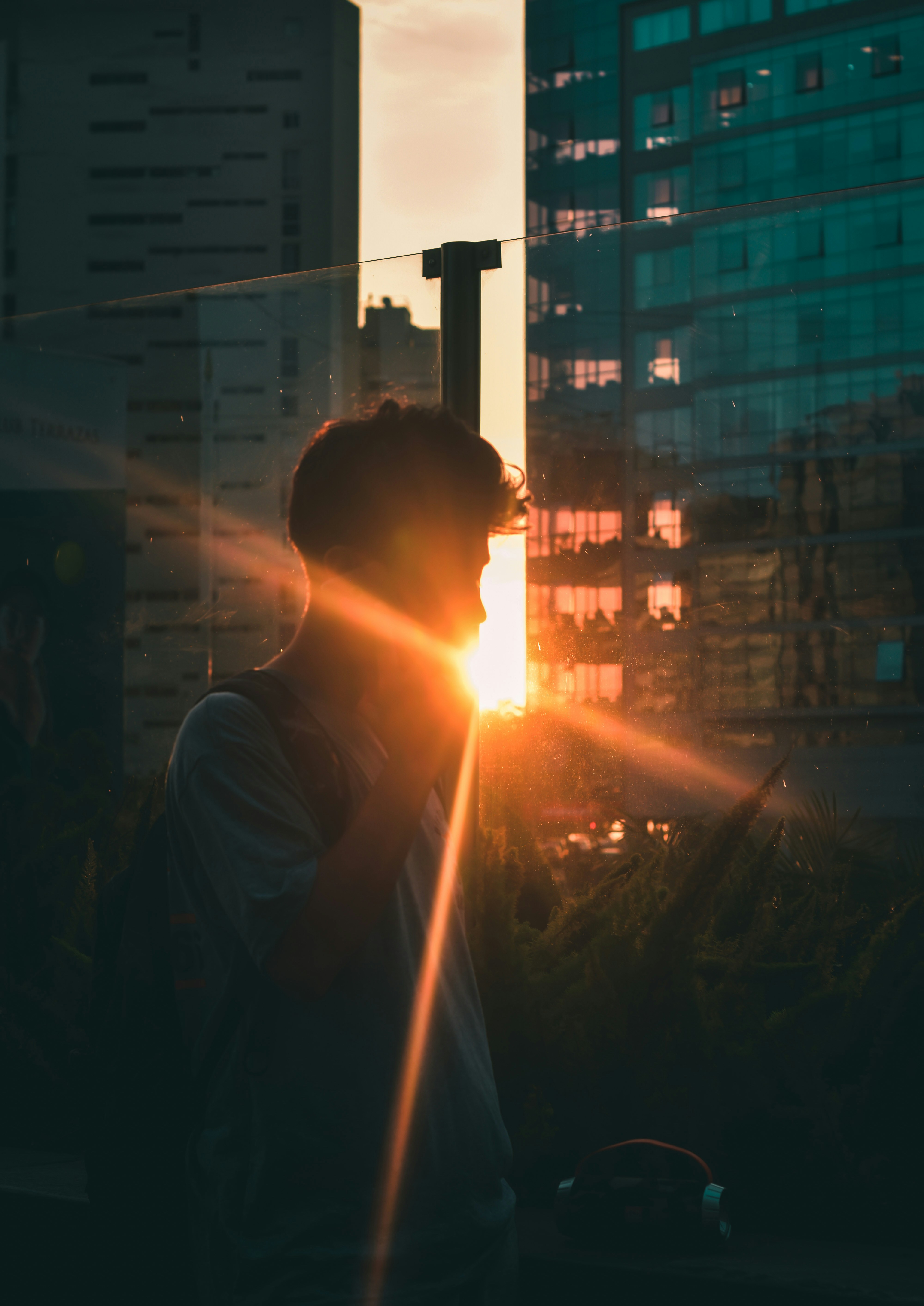 Silhouette of a person holding their chin, illuminated by the warm glow of the setting sun against a backdrop of urban architecture. 