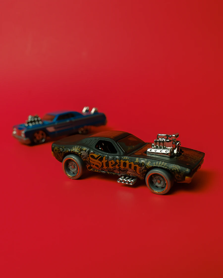 Two detailed toy muscle cars on a vivid red background, with a black car in sharp focus and a blue car blurred behind it.