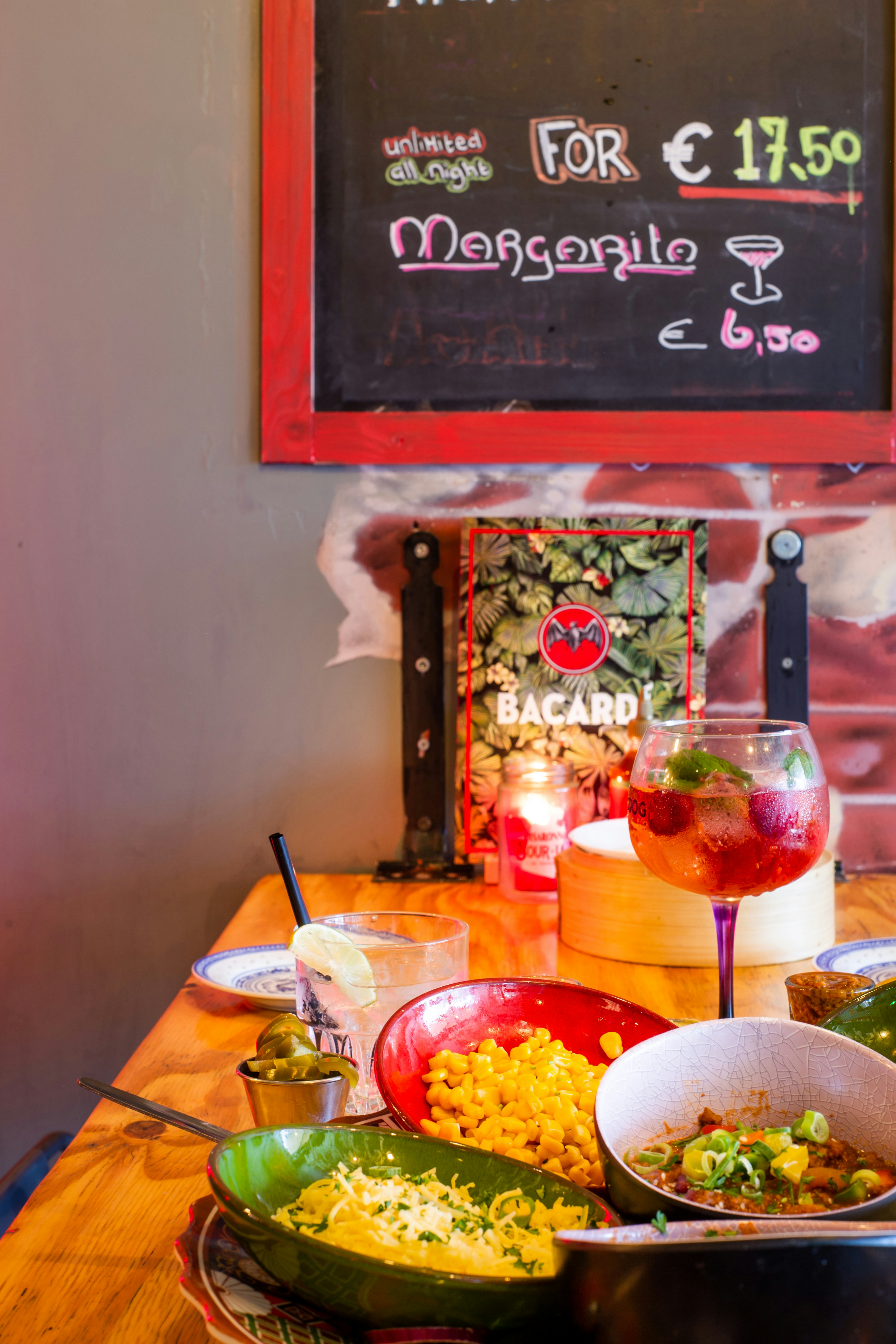 Colorful dishes arranged on a wooden table next to a chalkboard menu in a cozy restaurant setting.