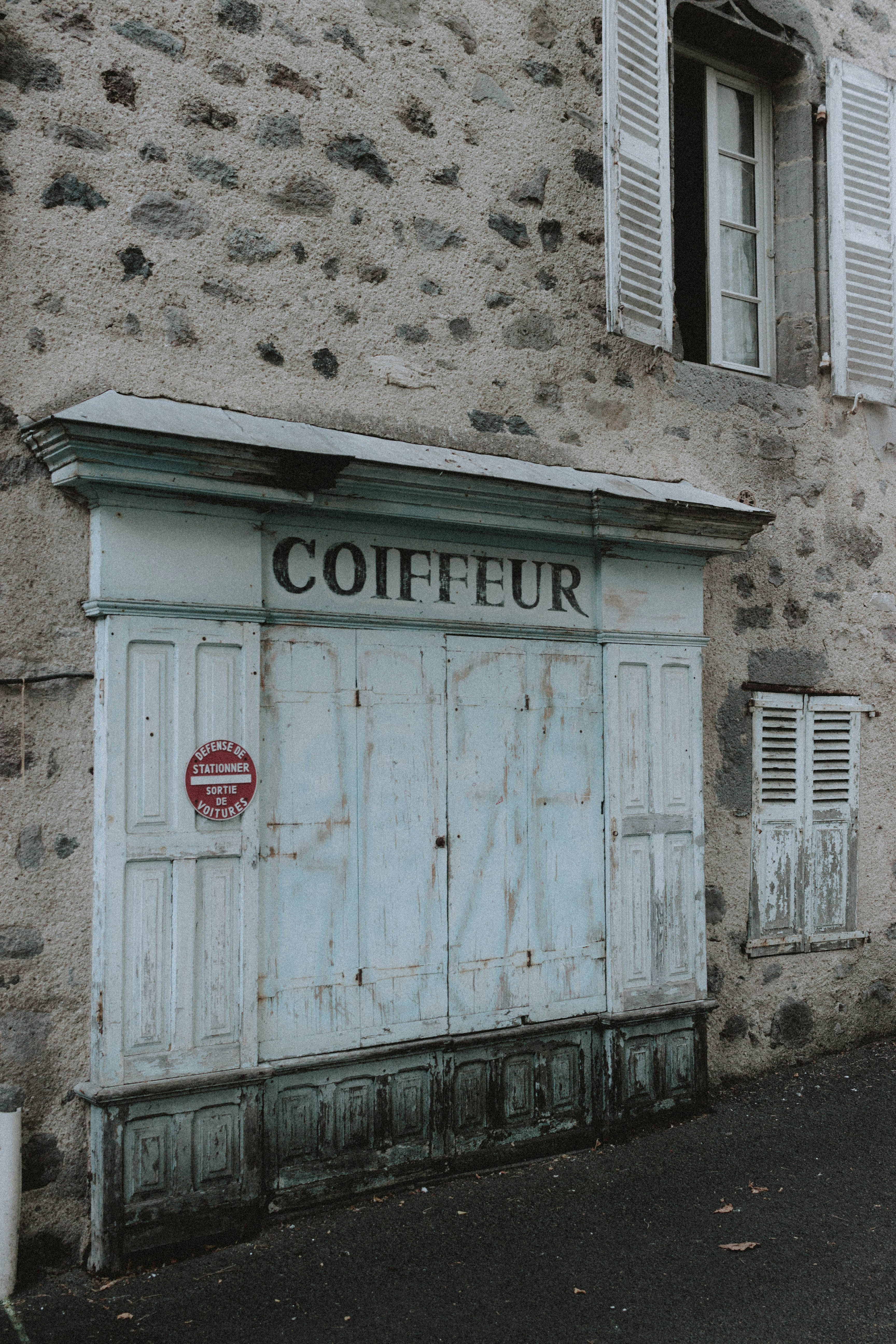Vintage storefront of a closed hair salon with faded blue paint and a red sign, set against a textured stone wall. The scene evokes nostalgia for the past.