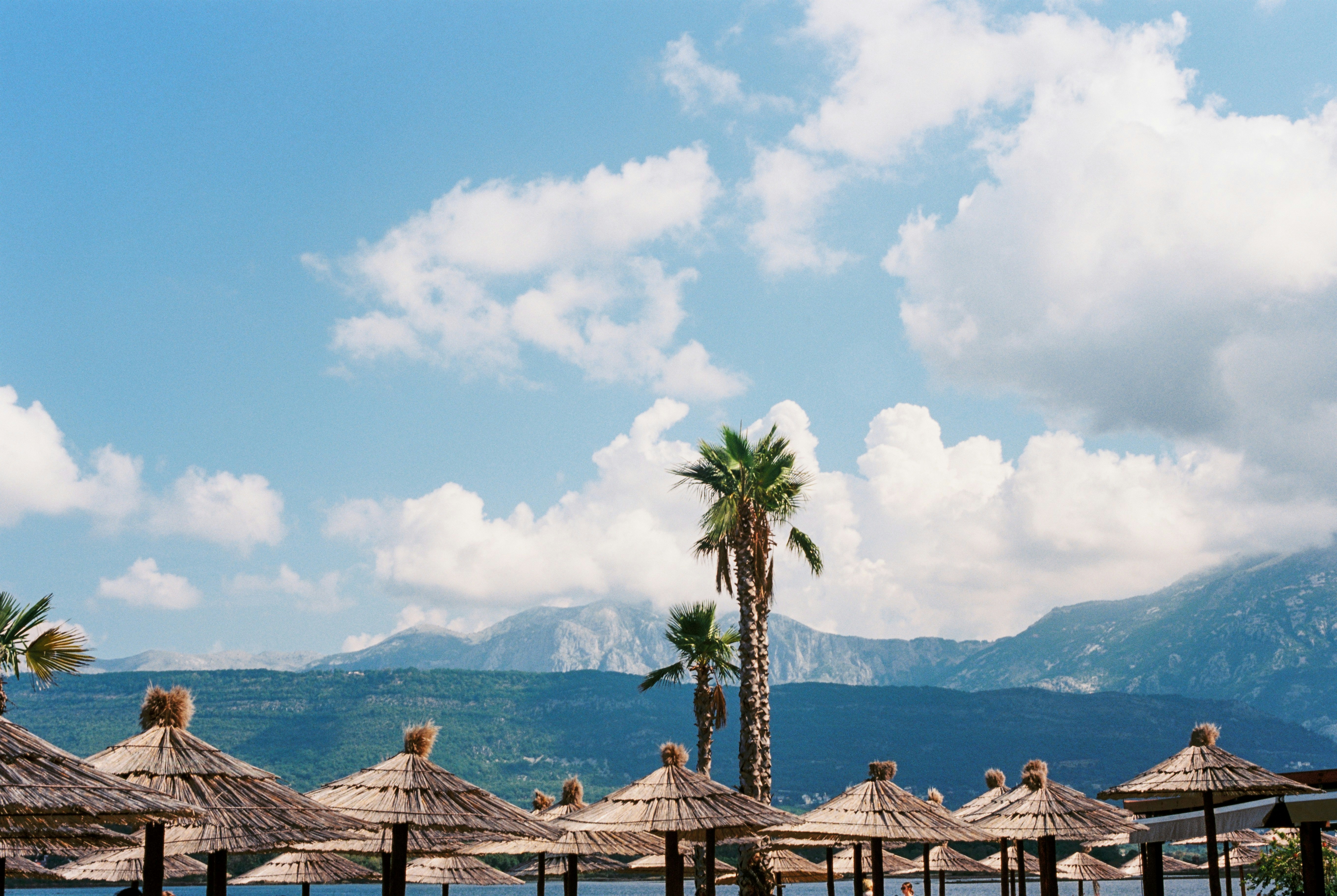 Thatched umbrellas under a bright blue sky with distant mountains.