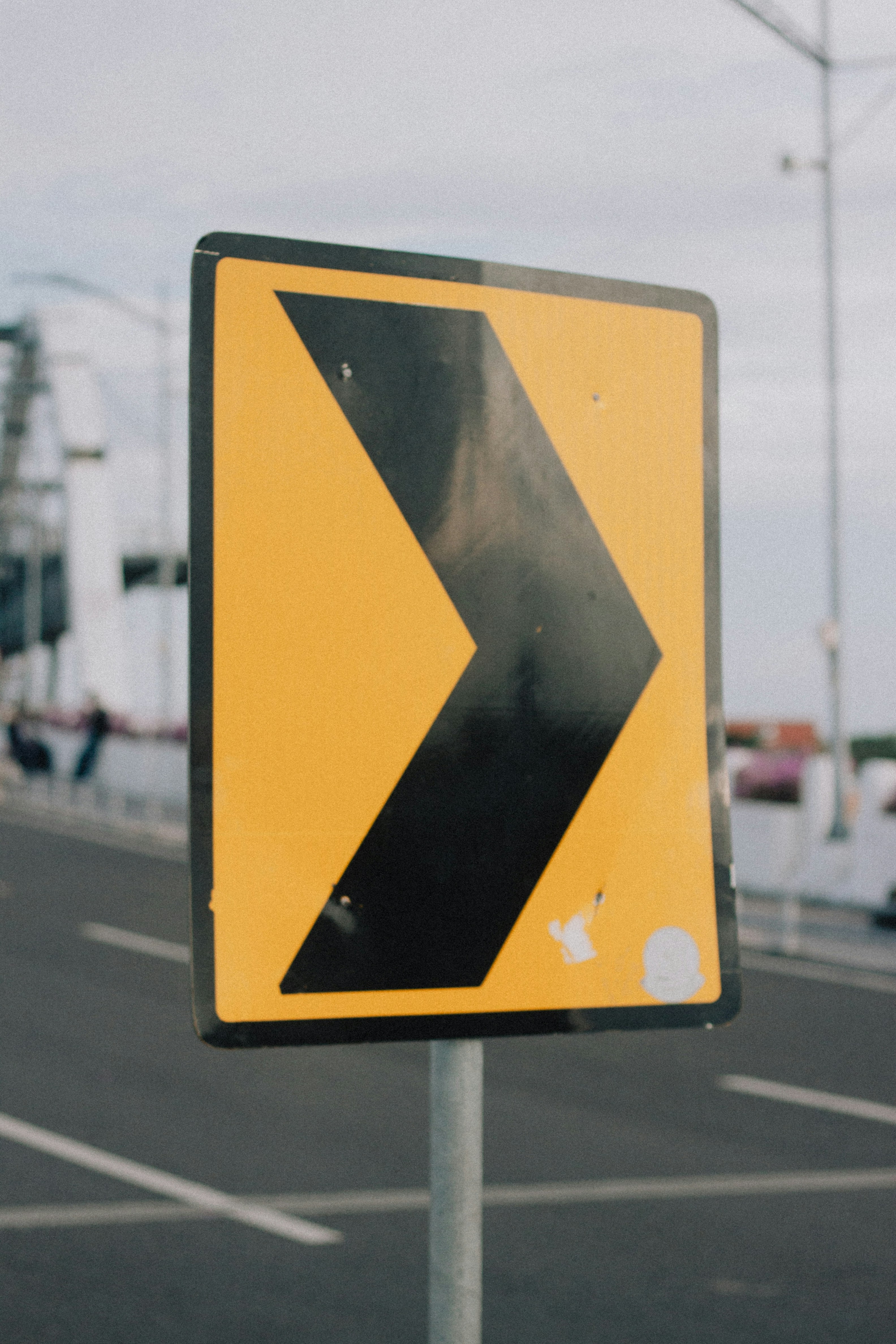 Curved road sign indicating a right turn, with visible wear and stickers on its surface.