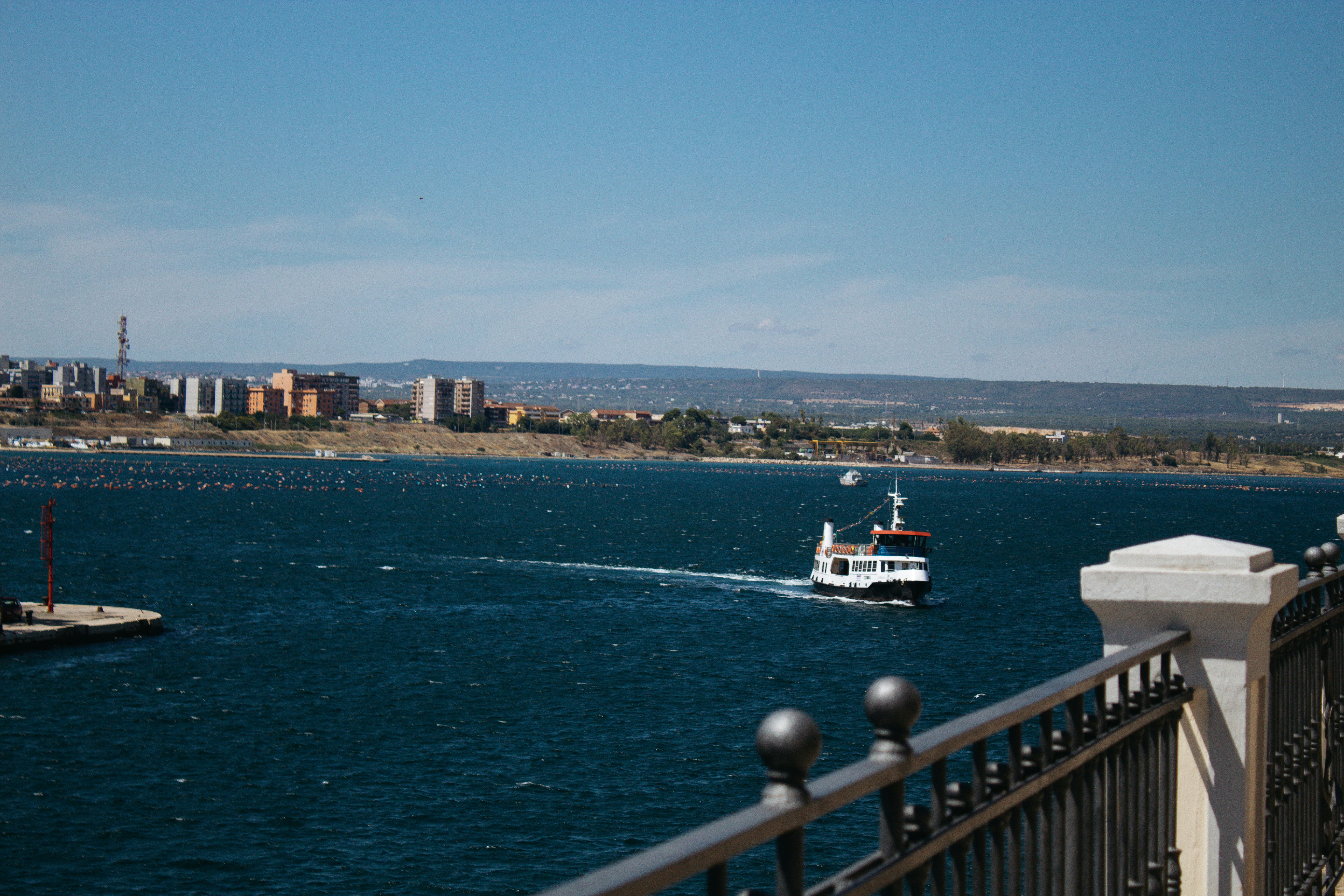Small boat navigating a deep blue harbor with a distant cityscape under a clear sky.