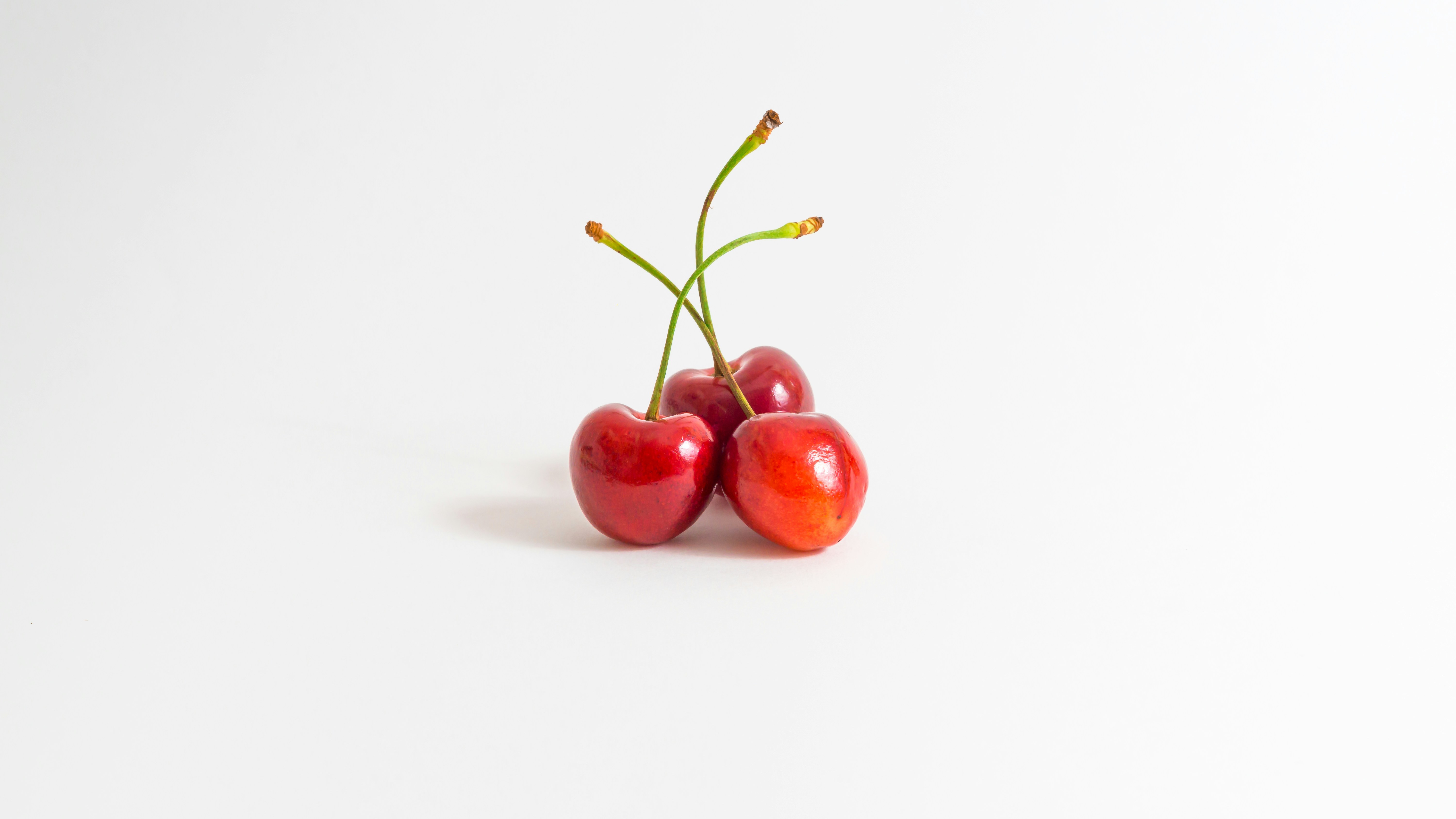 Three cherries on white background with smooth shadows. | 3 red cherries on white surface