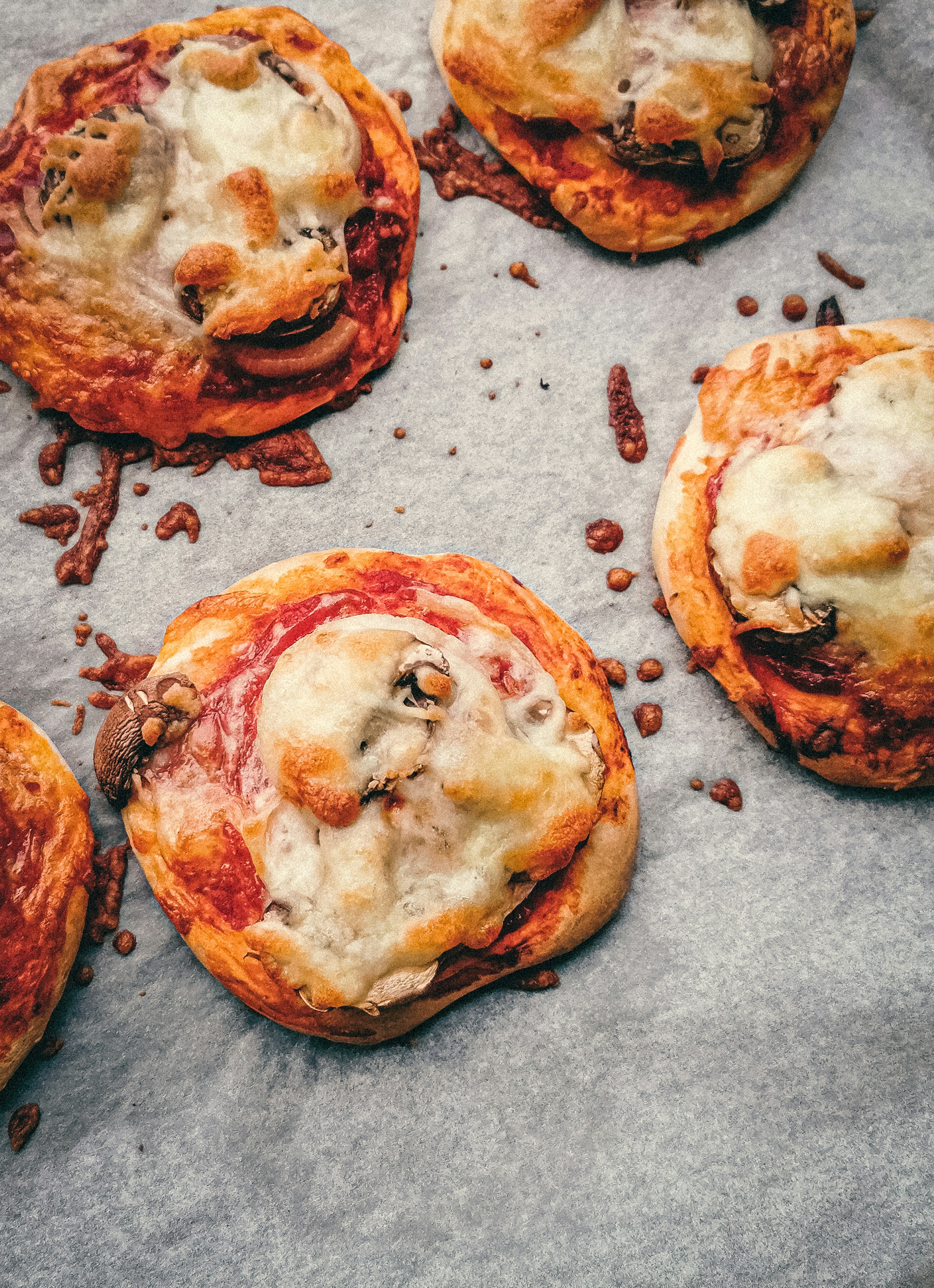 Top-down shot of four mini pizzas with melted cheese, tomato, and mushrooms on parchment.