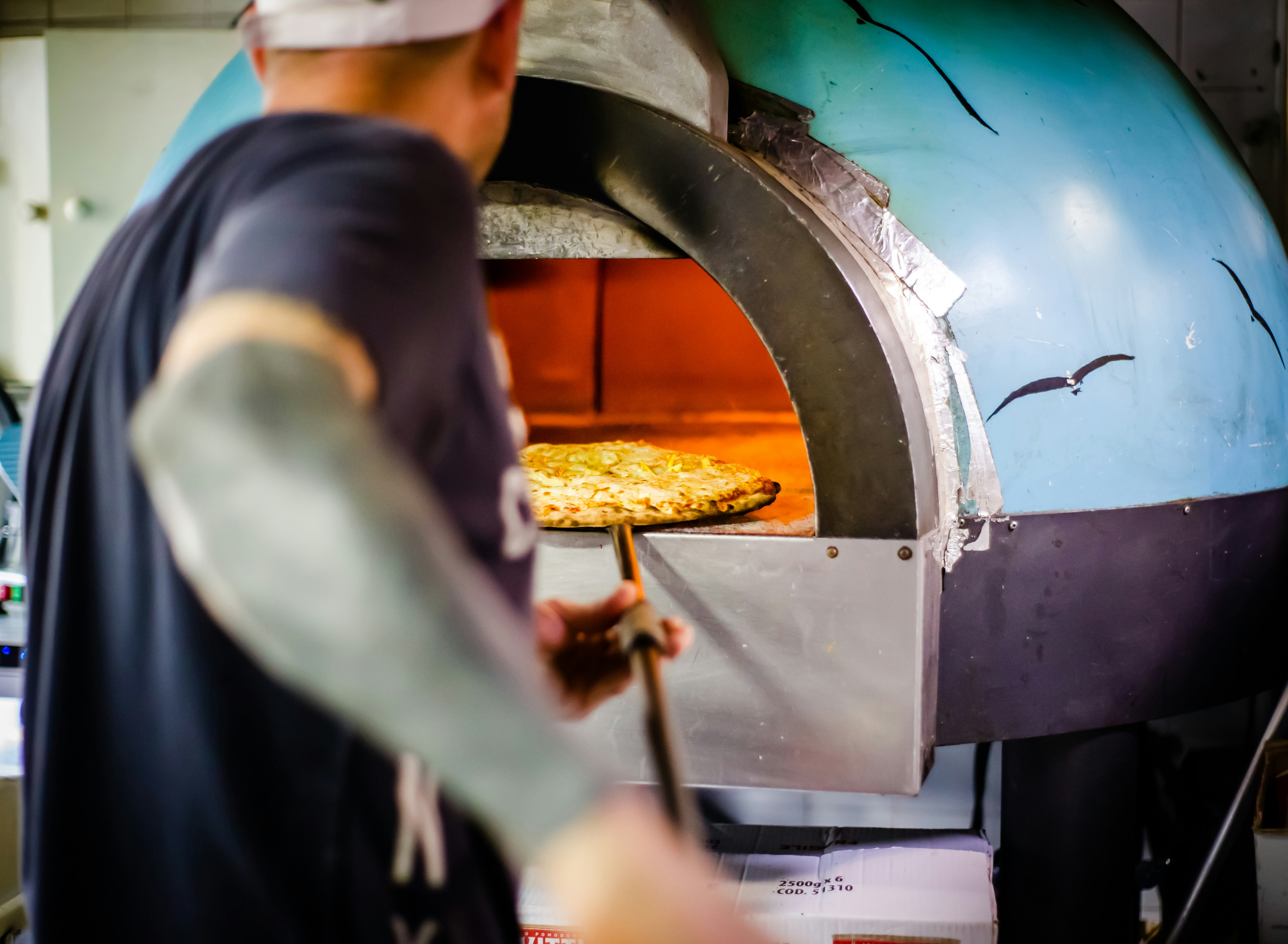 Chef placing pizza into a wood-fired oven, flames glowing warmly.