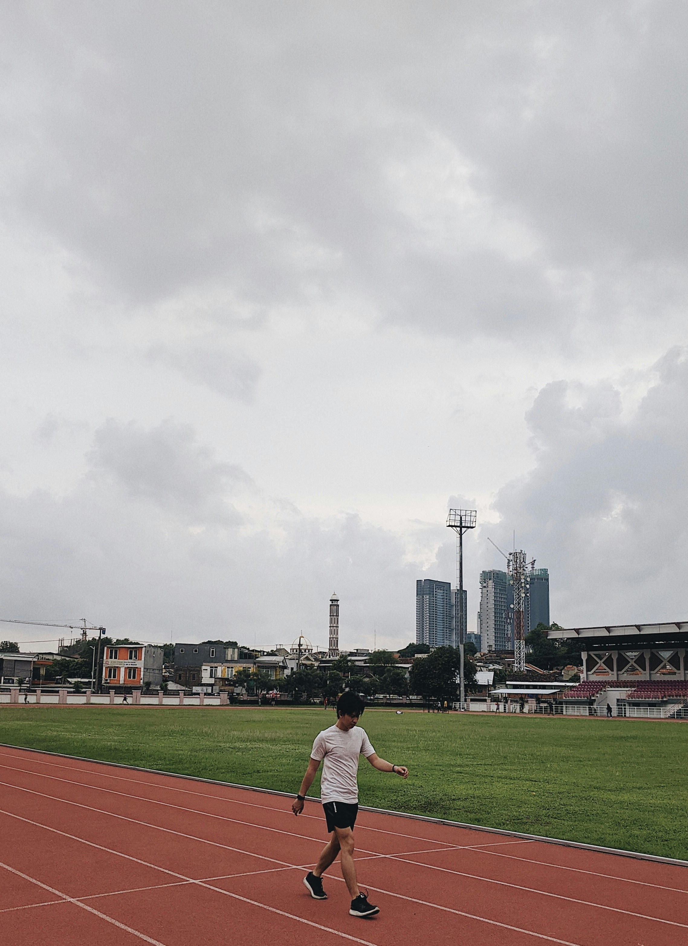 Footsteps on a Red Track as City Towers Rise Beyond the Field