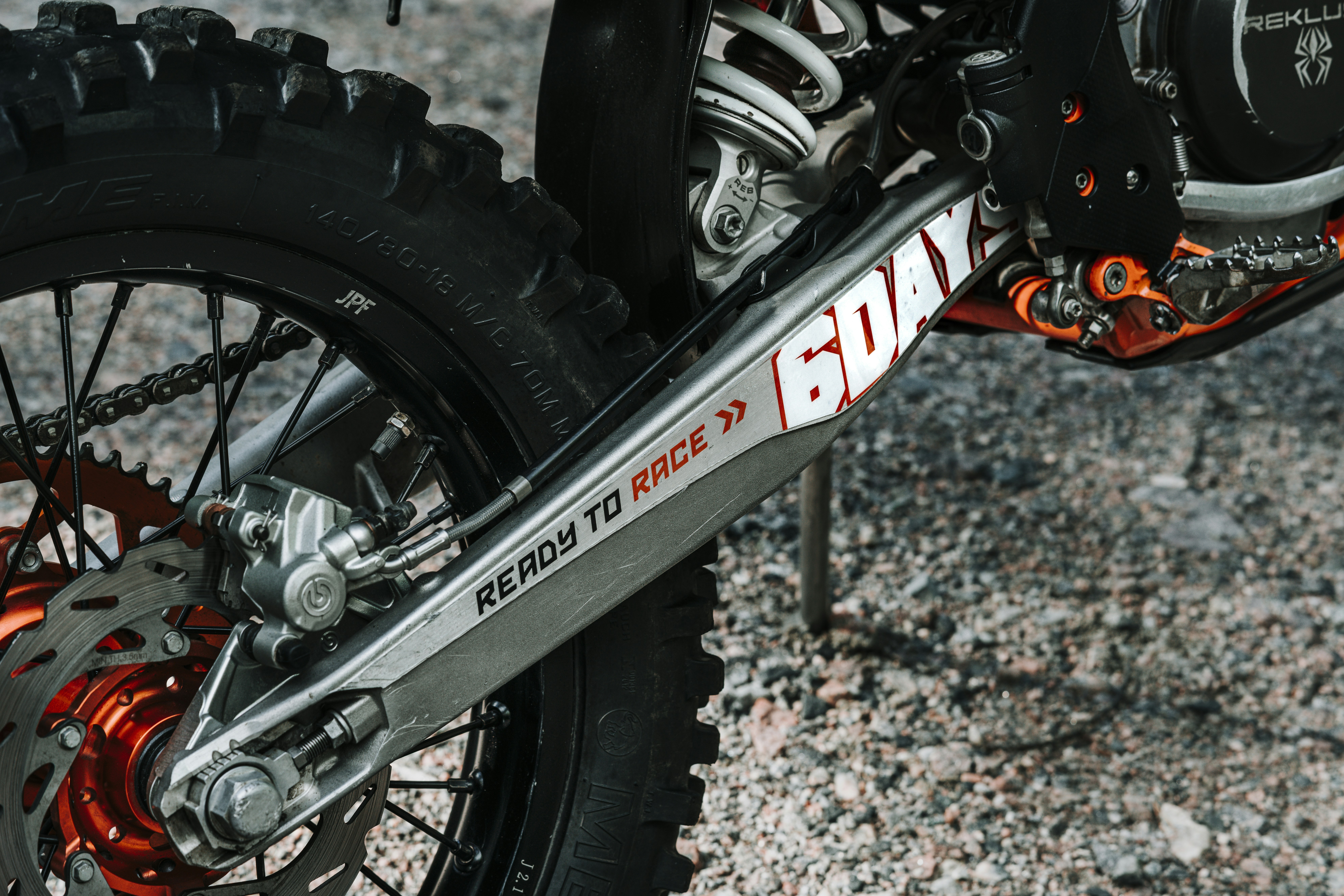 Close-up of a motorcycle's rear swingarm showcasing the 'READY TO RACE' slogan and intricate mechanical details.