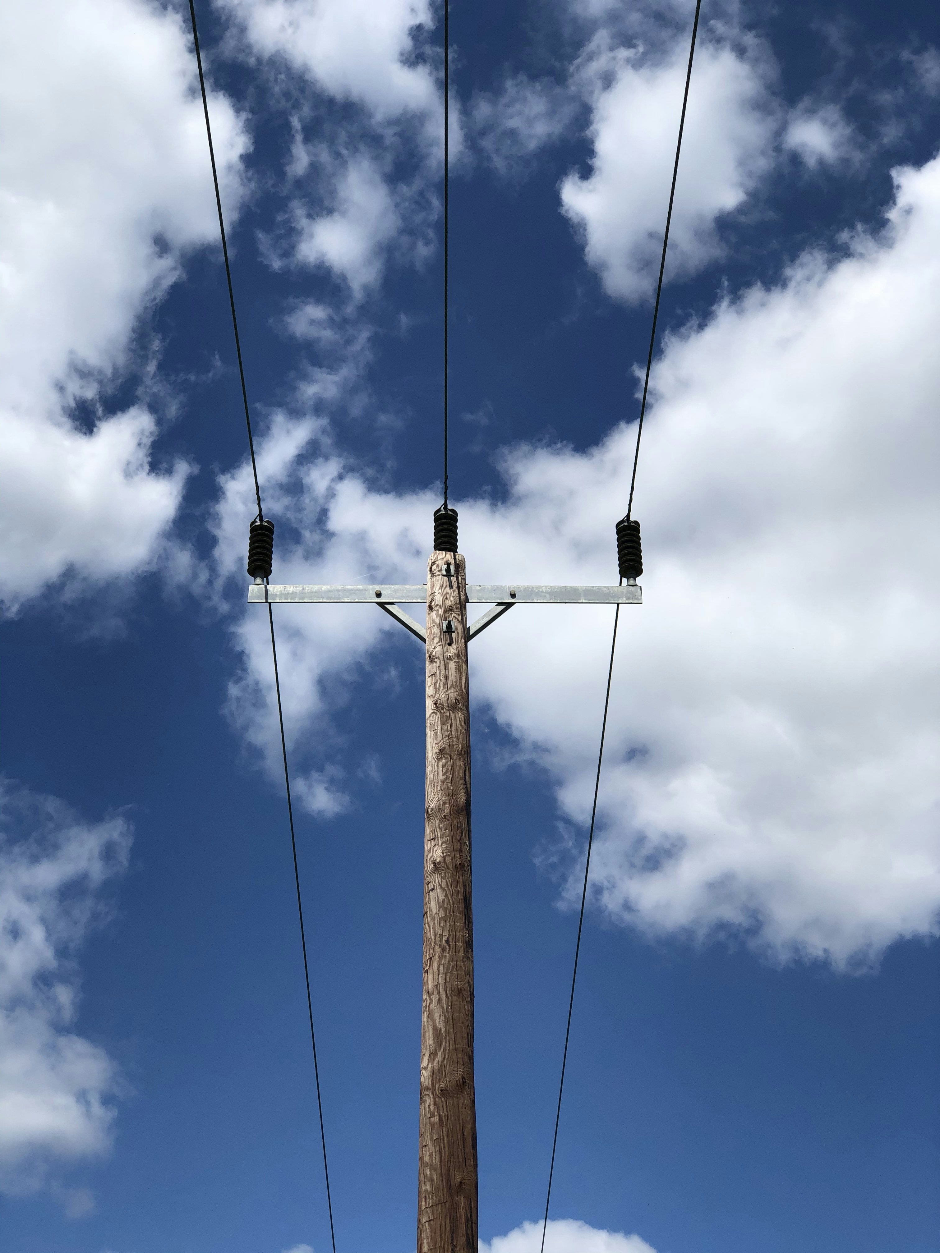 Utility pole extending upward, intersected by power lines against a backdrop of vibrant blue sky and fluffy white clouds.