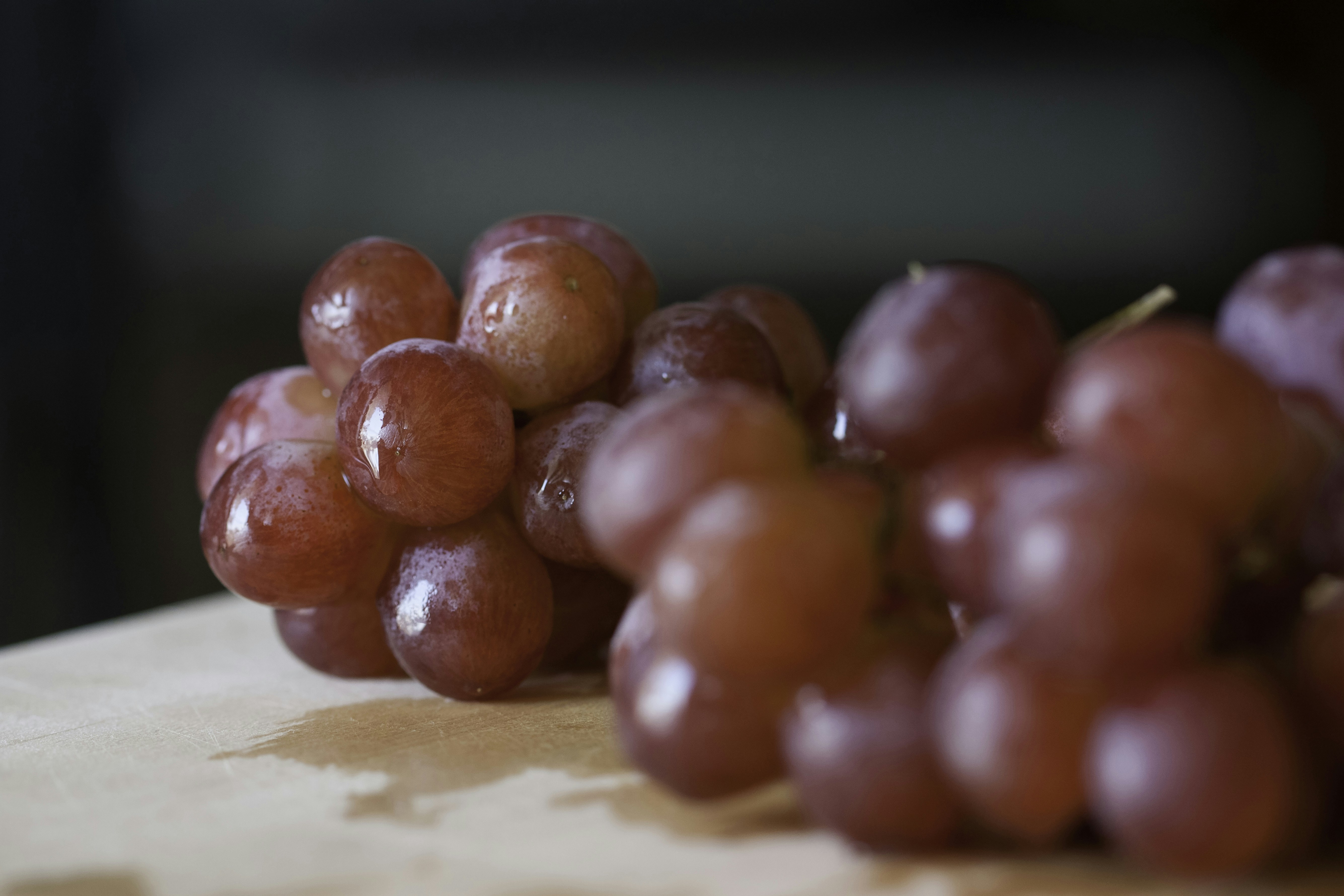Cluster of fresh red grapes glistening with droplets of water, resting on a wooden surface.