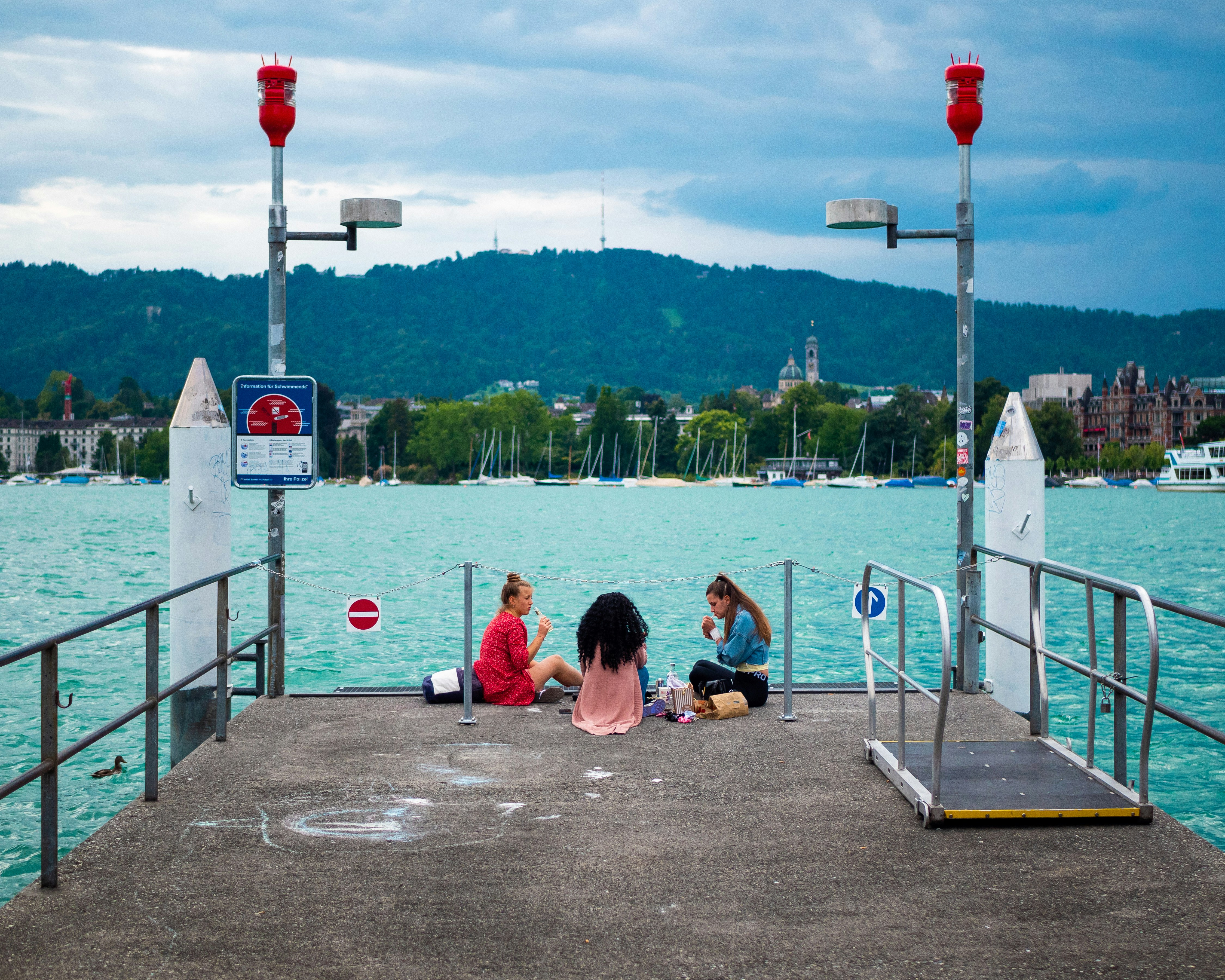 Three friends enjoying a leisurely afternoon on a waterfront pier, surrounded by serene waters and distant mountains.