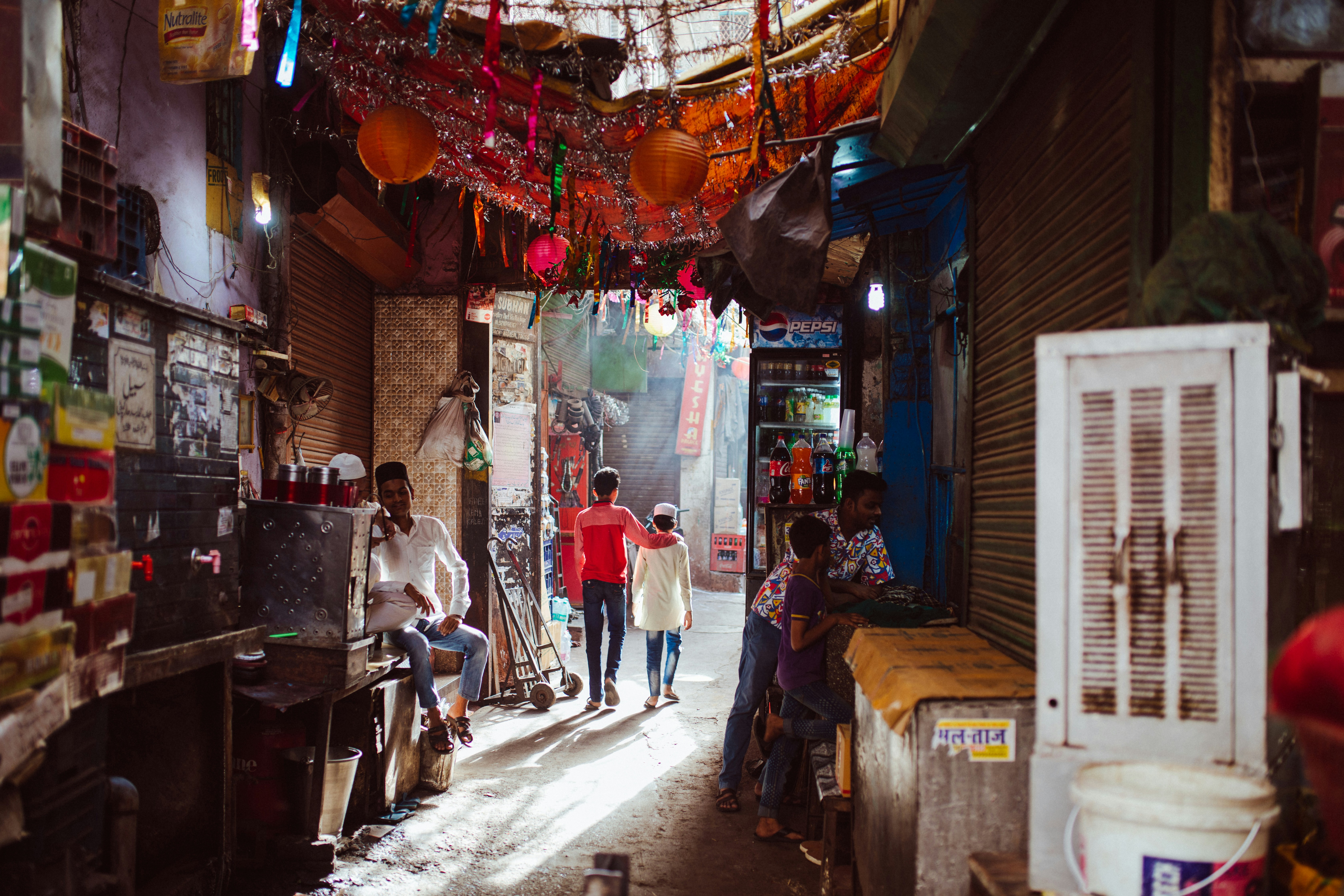 Colorful market alley bustling with people and vibrant hanging decorations.