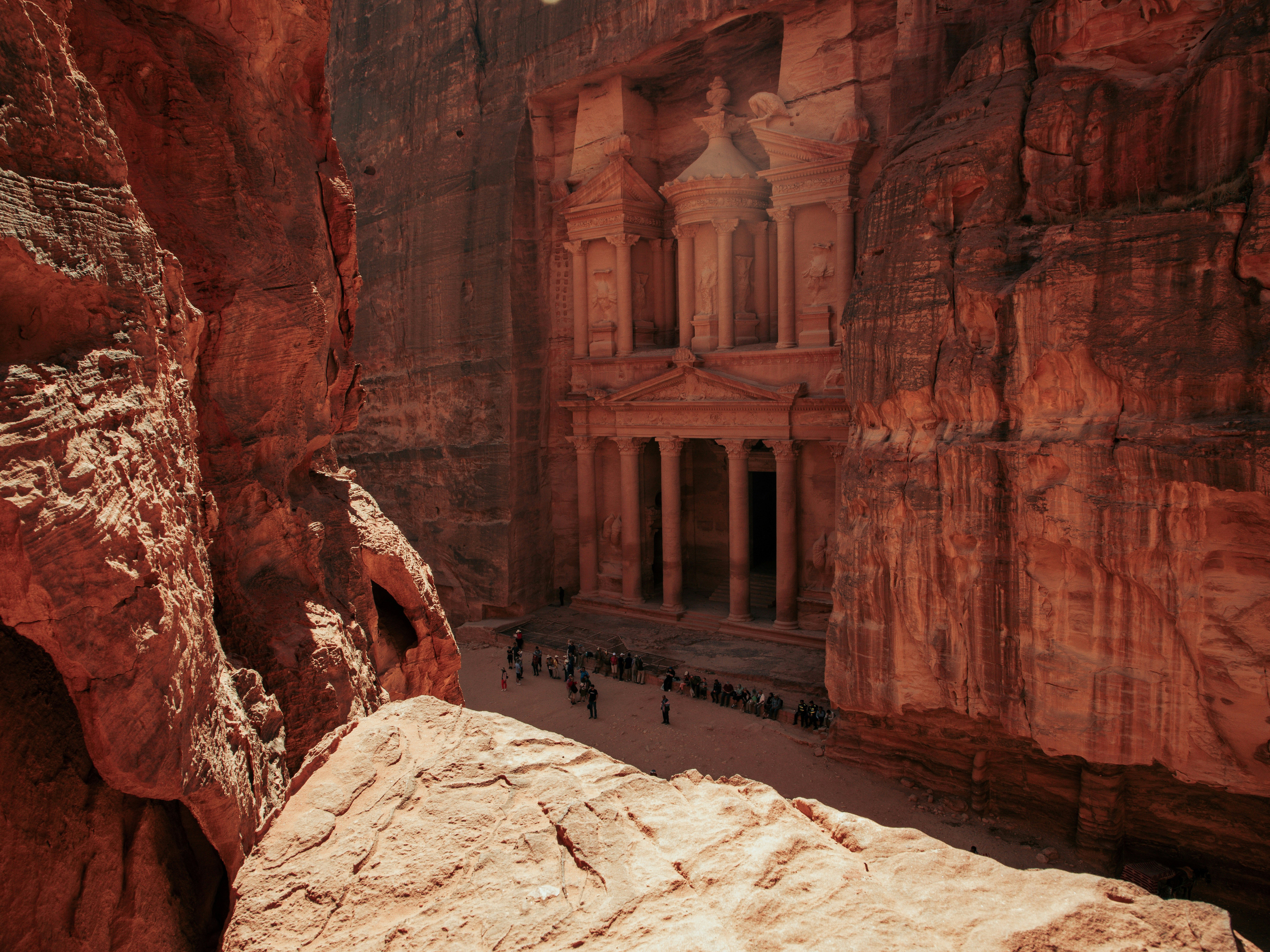 Sunlit Petra facade emerges from towering sandstone cliffs.