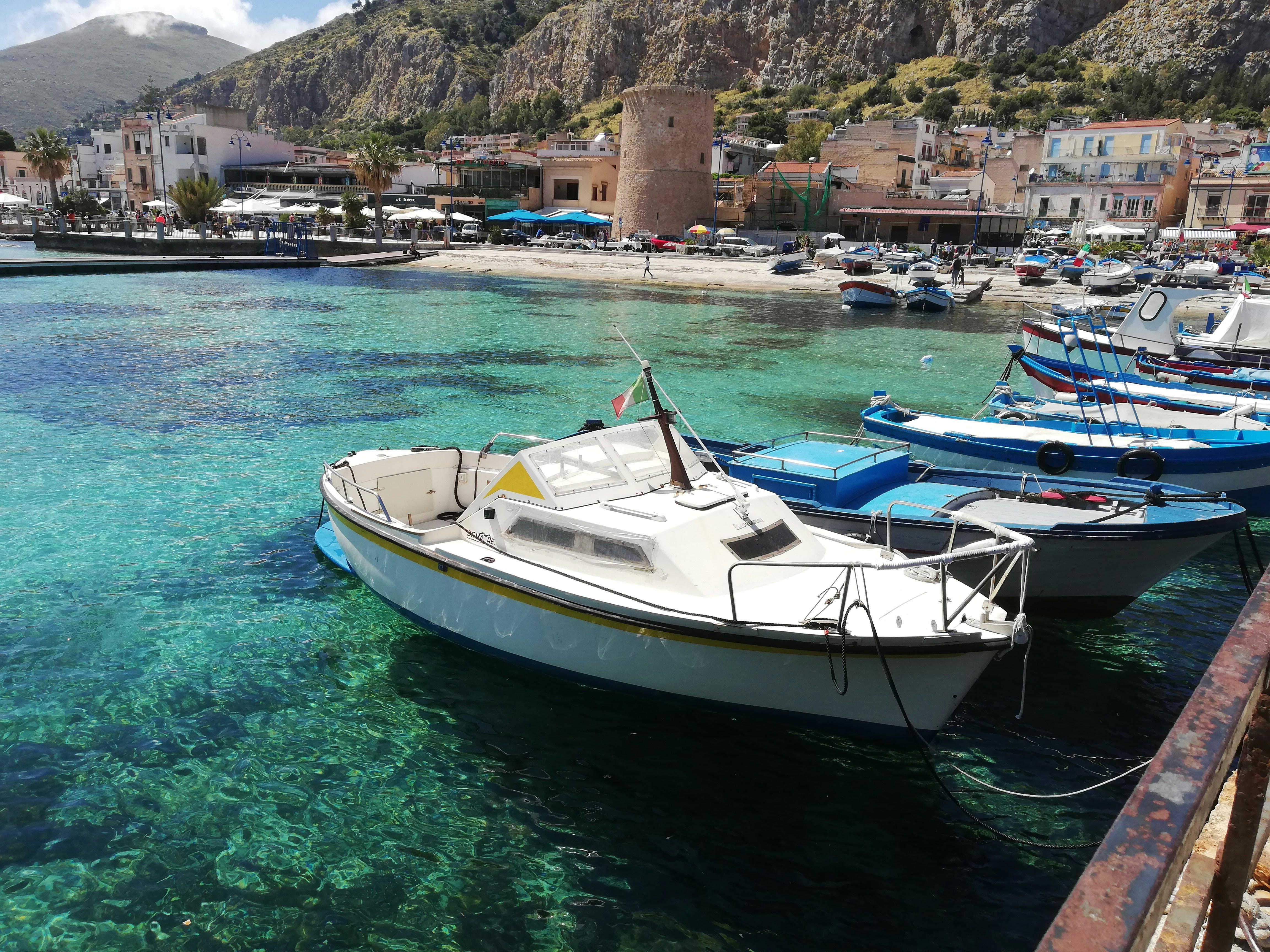 White boat moored in clear turquoise waters with a backdrop of mountains and coastal town.