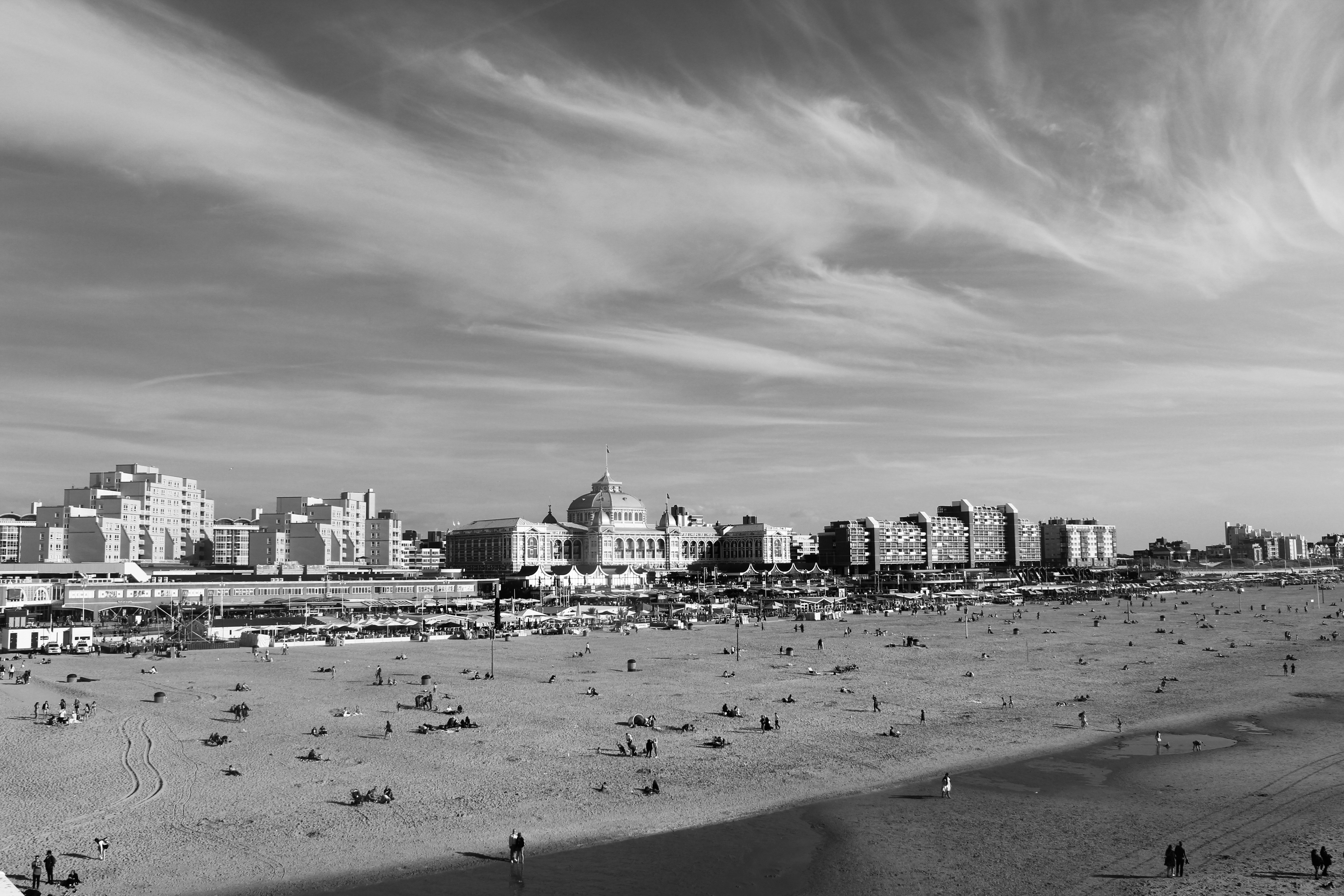 Expansive beach with scattered visitors under dramatic cloud formations and a distant coastal skyline.