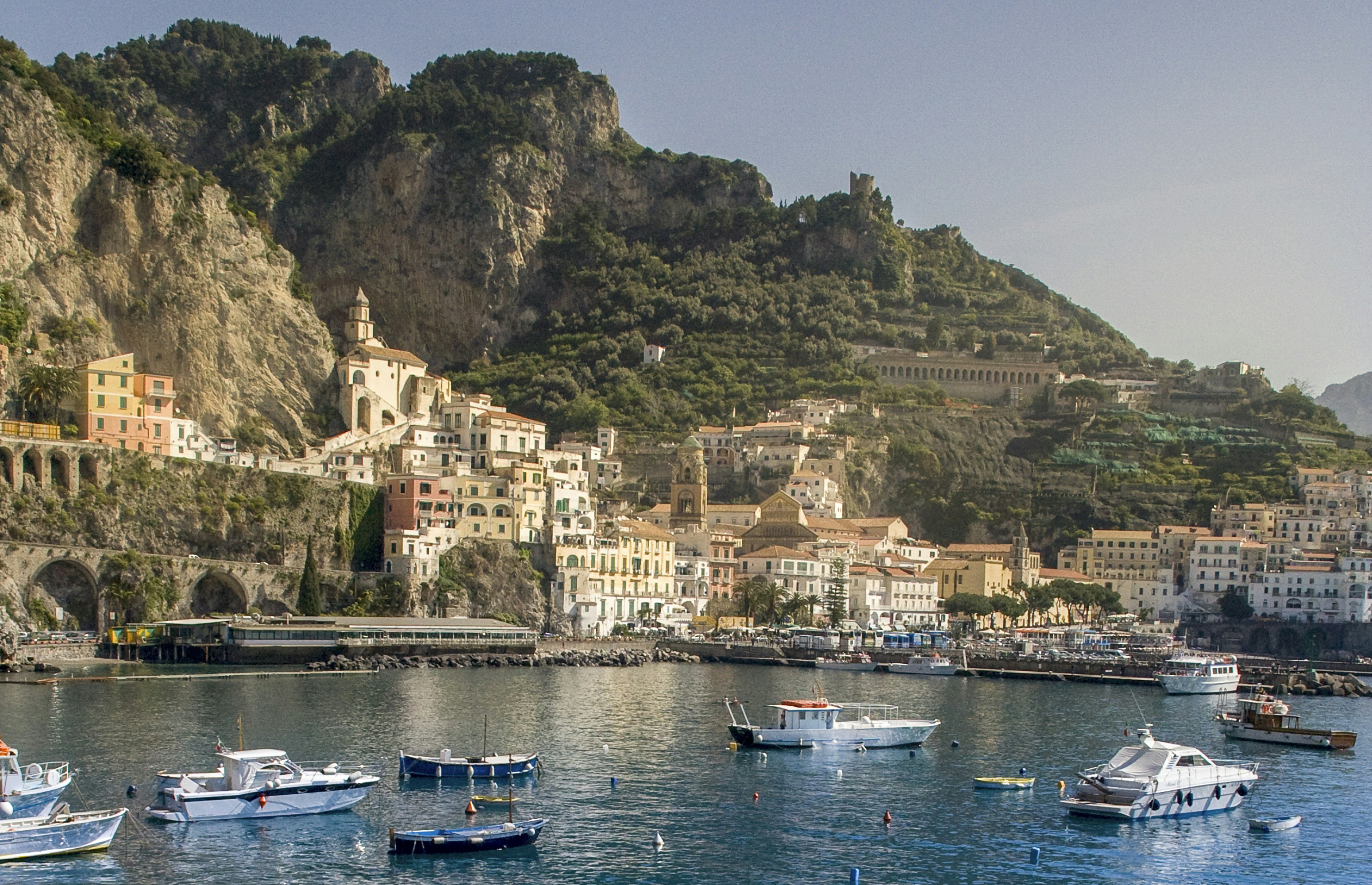 view of boats in amalfi harbor and town | white and blue boat on water near brown and green mountain during daytime