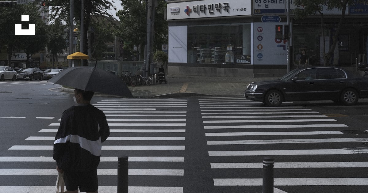 낮 동안 보행자 차선을 걷는 우산을 들고 있는 흑백 재킷을 입은 사람 사진 Unsplash의 무료 서울 이미지