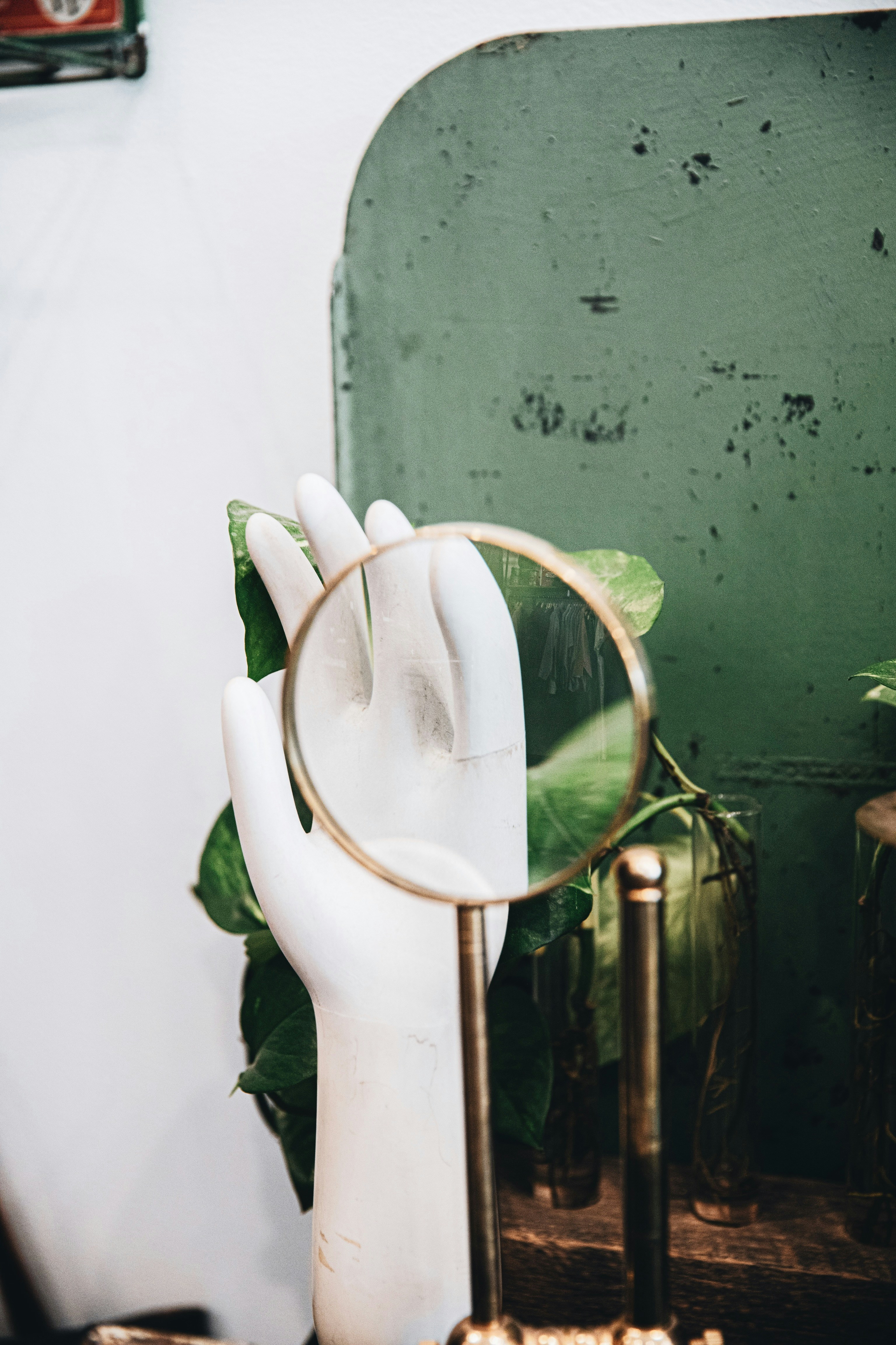Circle of Focus: A Brass Magnifier Framing a White Mannequin Hand Against an Aged Green Backdrop