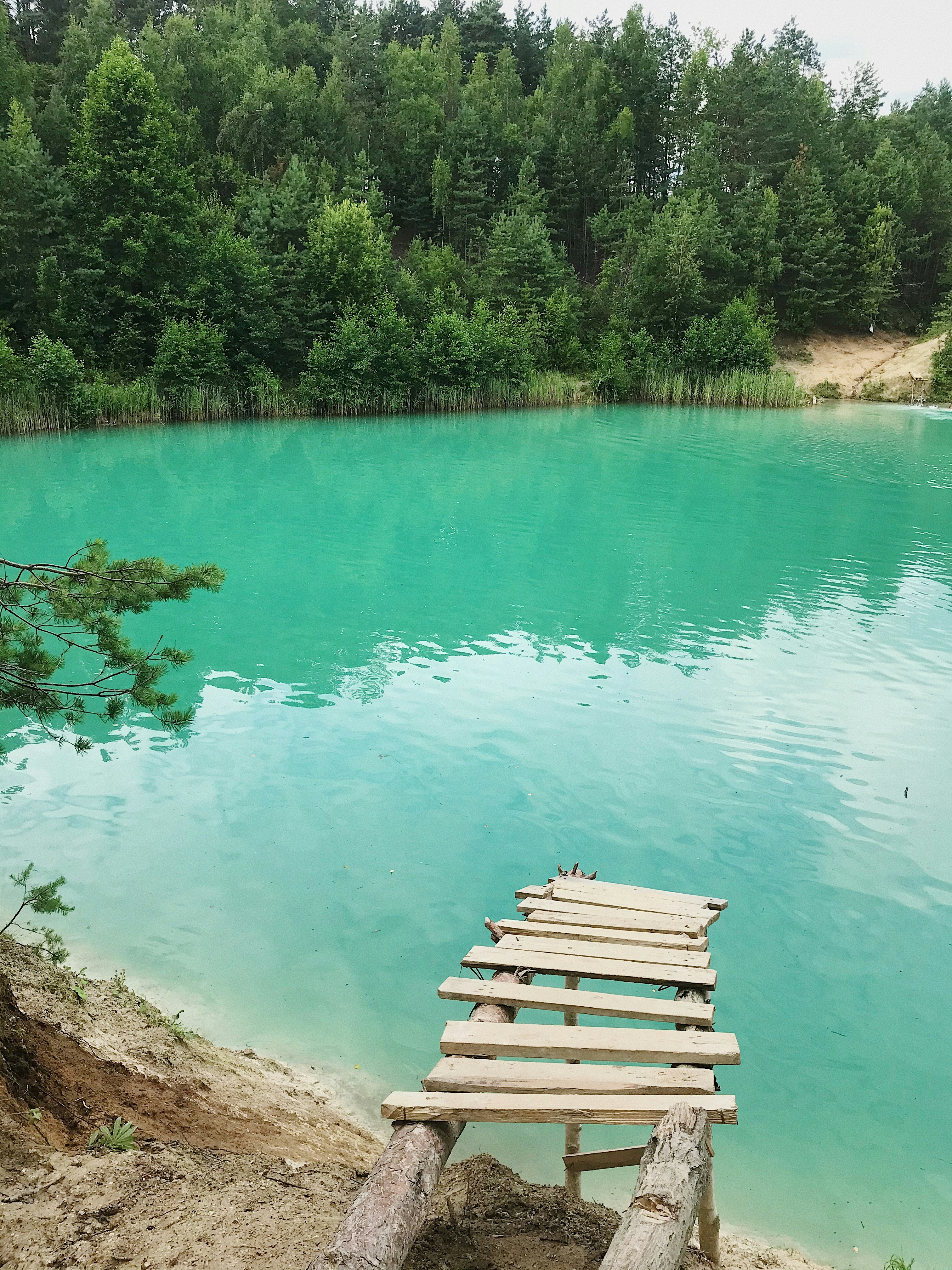 Wooden pathway leading to a tranquil turquoise lake surrounded by lush greenery. The scene invites contemplation and relaxation.