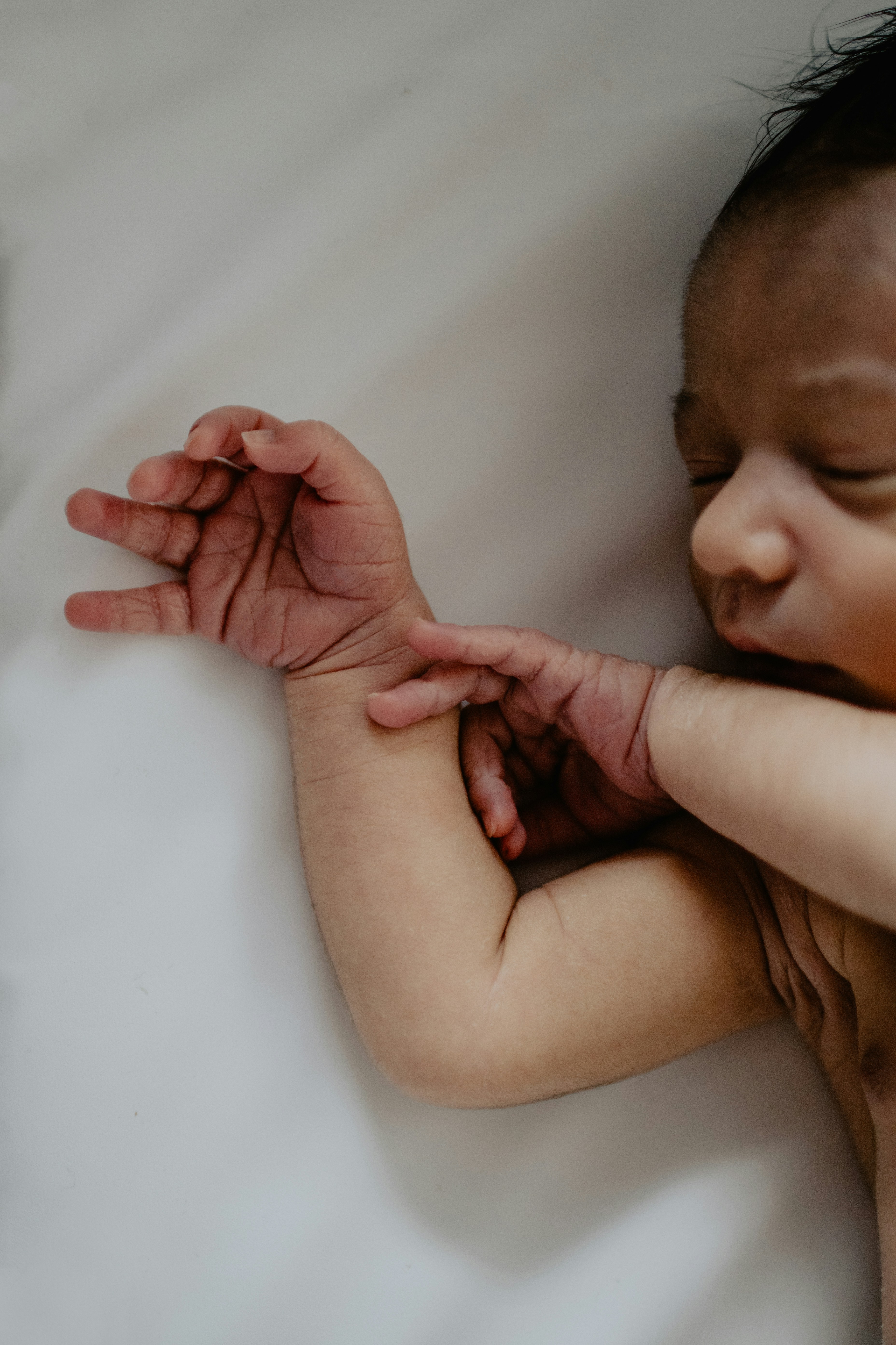 Close-up of a sleeping baby's hands resting on a soft surface, showcasing delicate features and peacefulness.