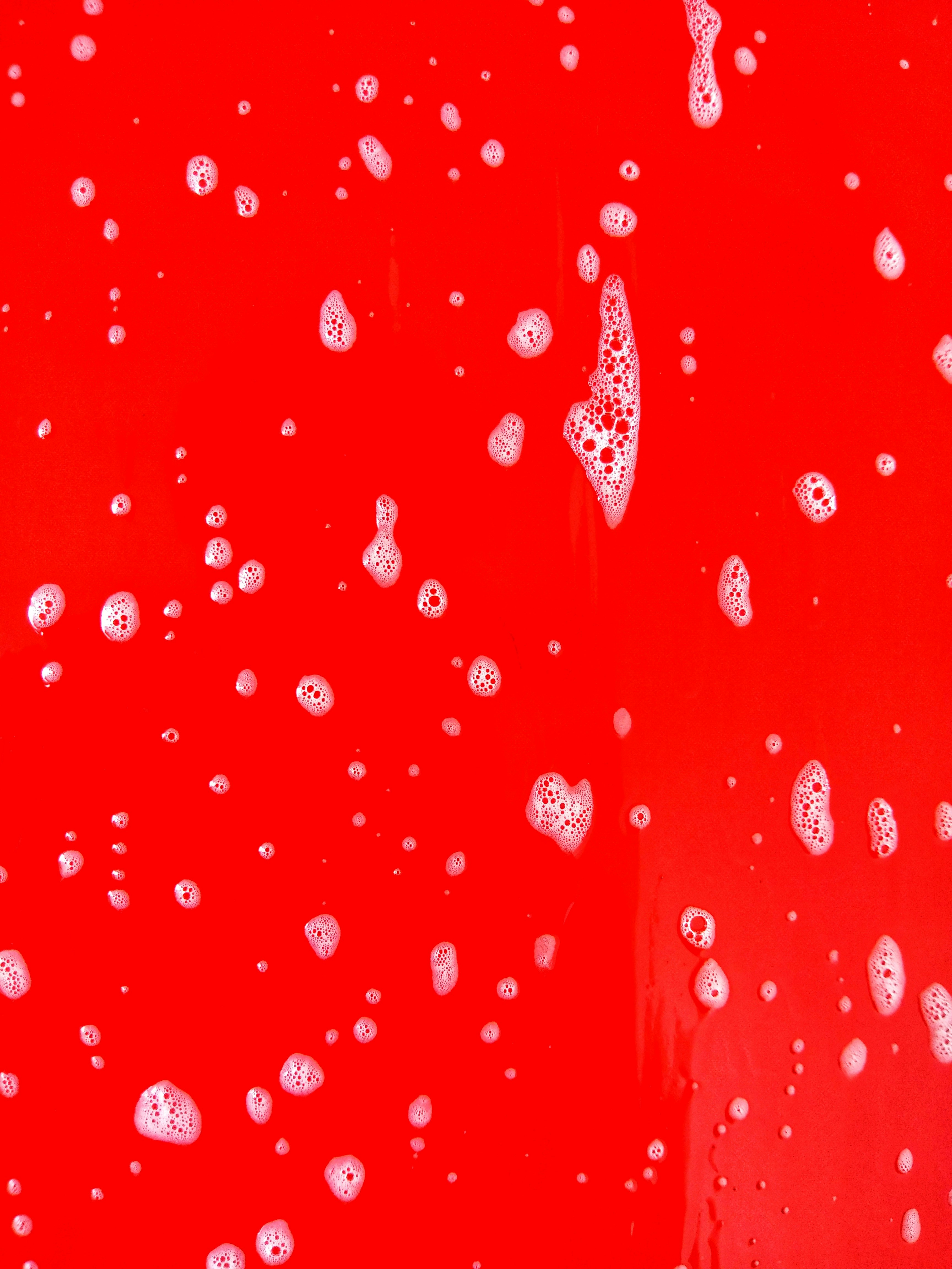 Vibrant red surface adorned with clusters of white bubbles, creating an abstract visual texture.