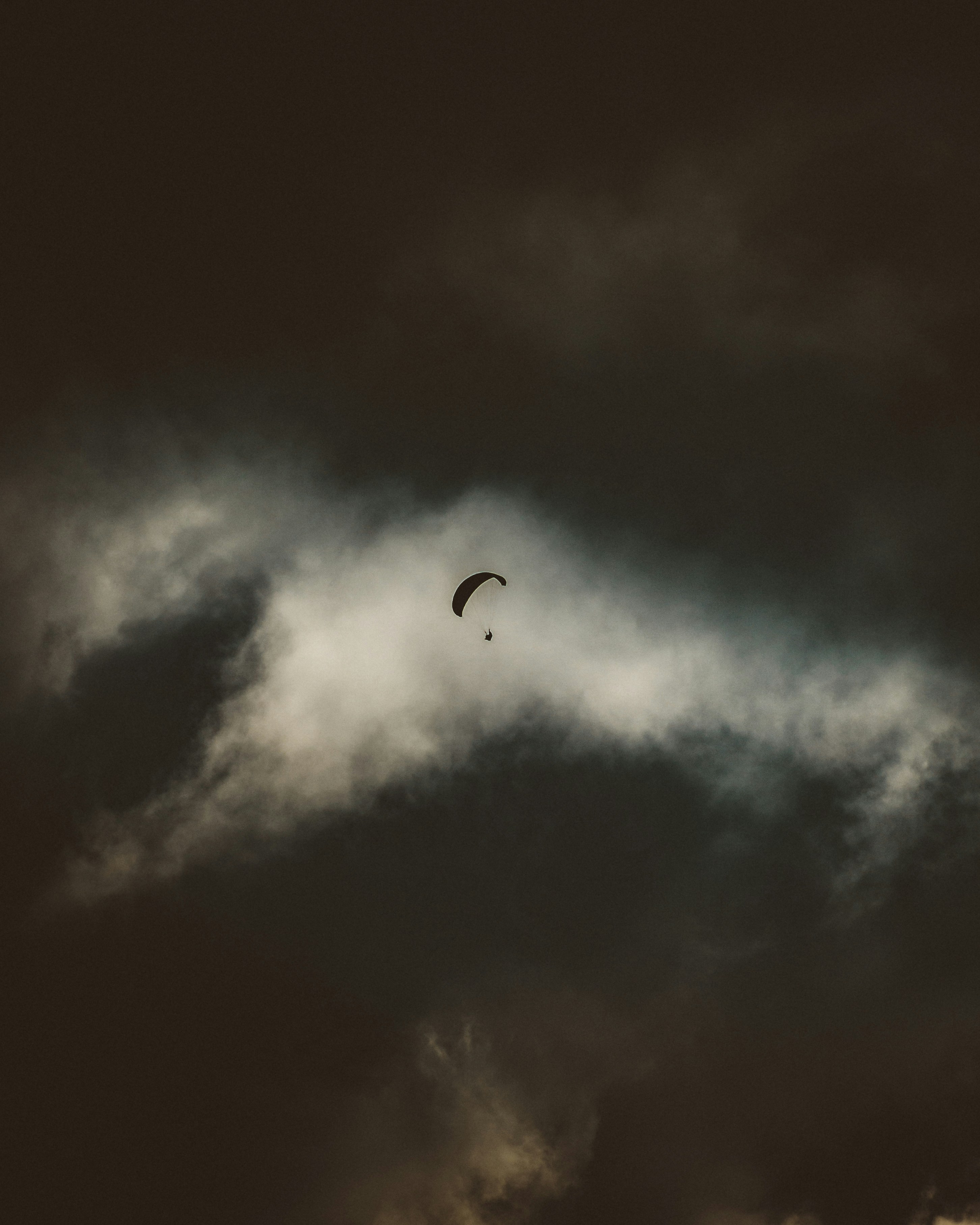 A lone paraglider navigates the moody skies, silhouetted against dramatic clouds. The scene captures the essence of freedom and adventure.
